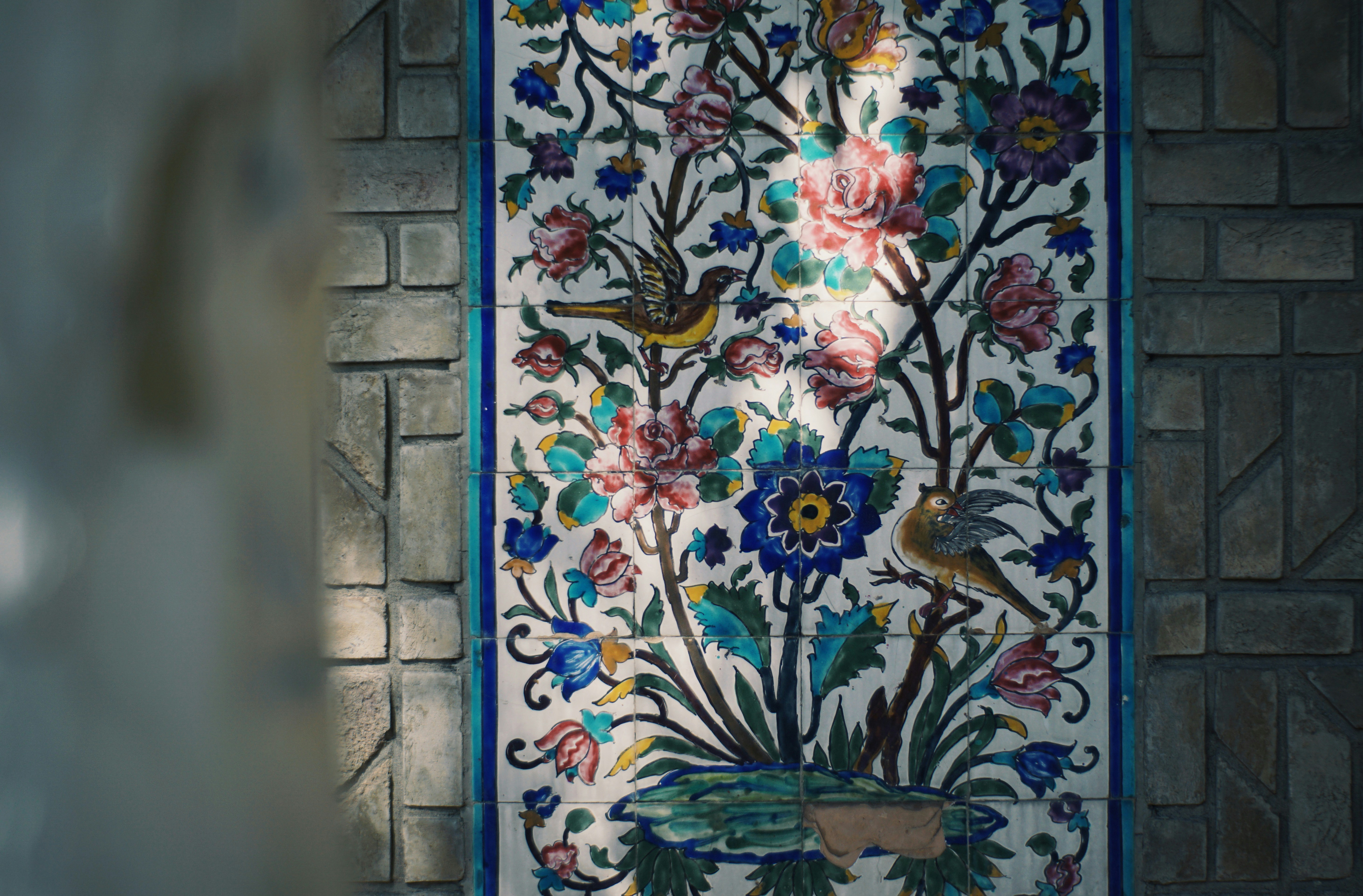 Intricate floral mosaic featuring vibrant roses and birds against a textured background. The design showcases skilled artistry in ceramic decoration.