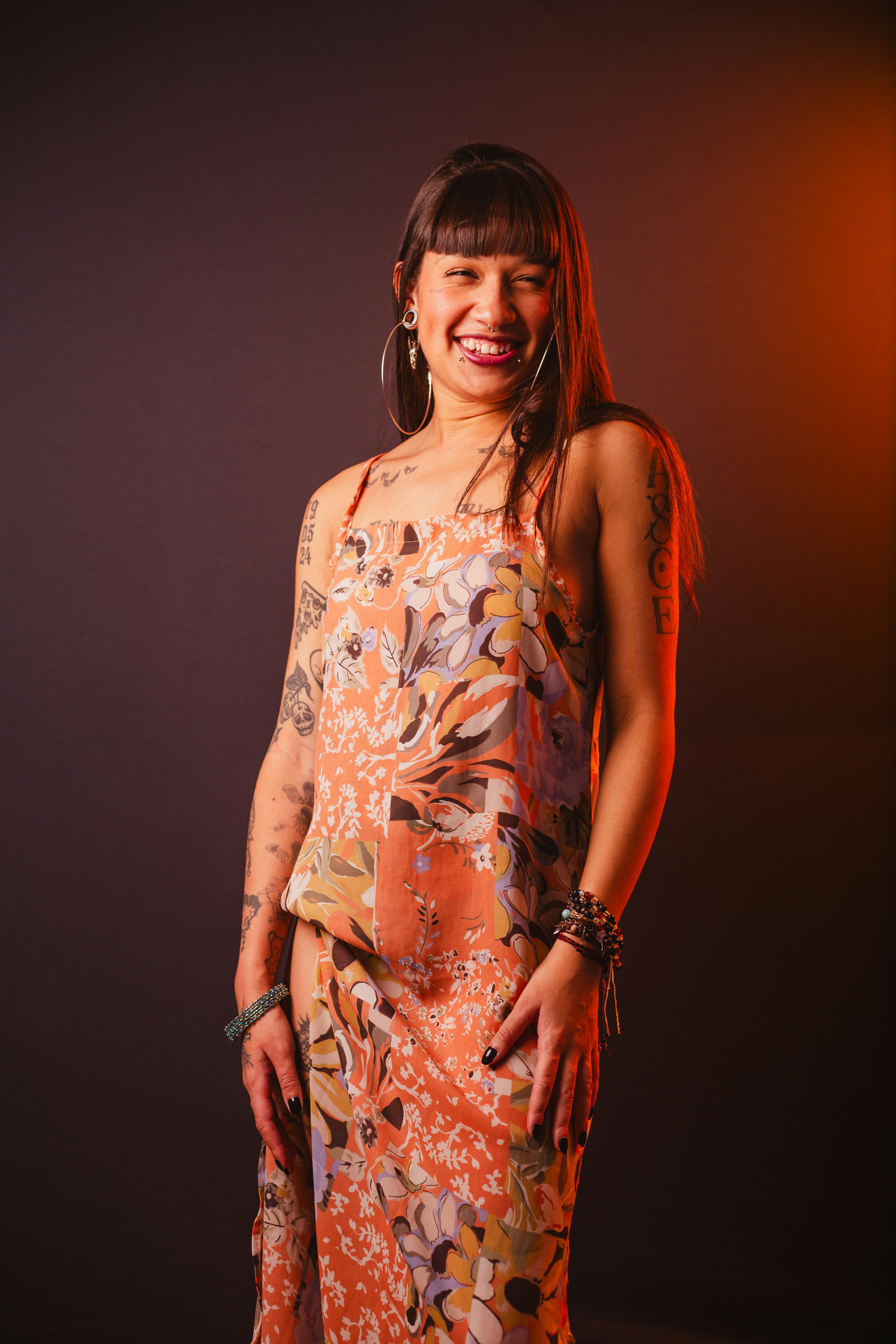 Woman with tattoos smiling against a dark background.