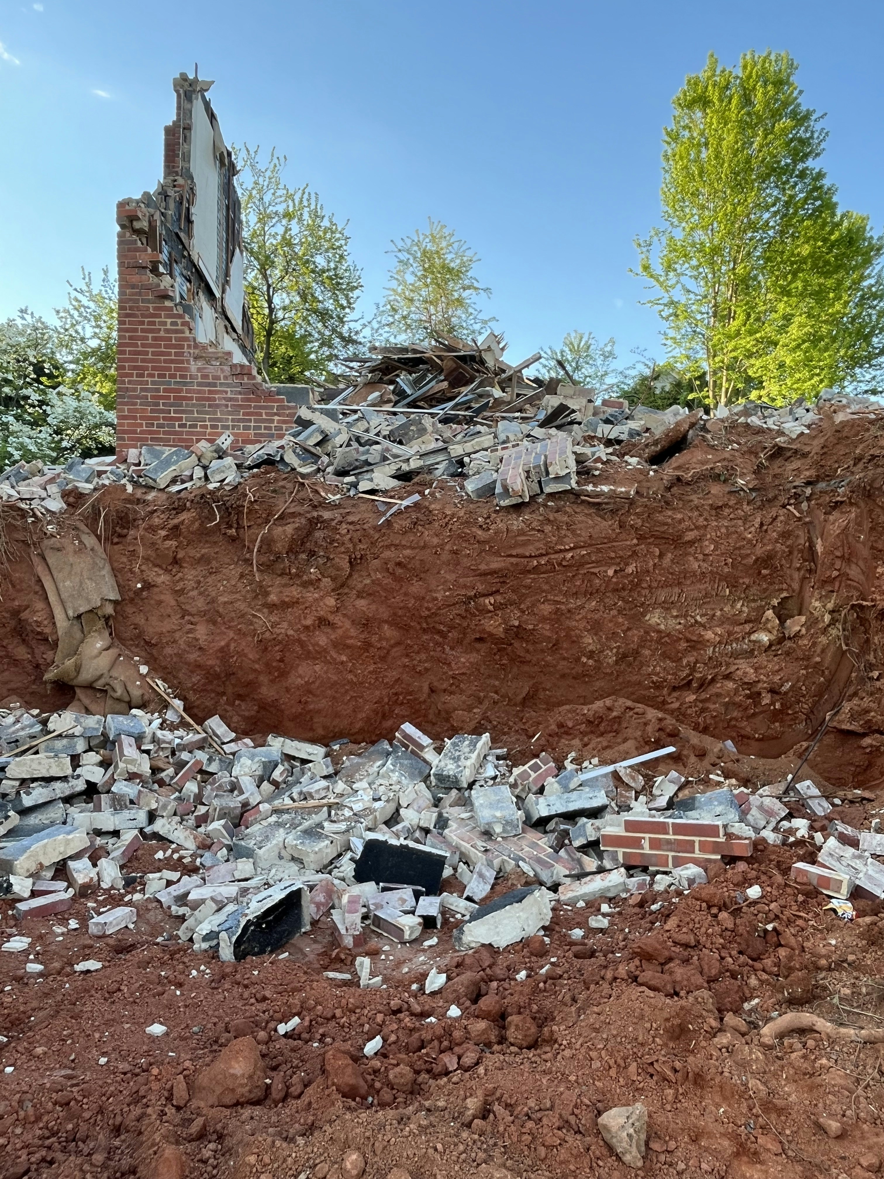 A demolition site of a house | Ruins of a brick building with debris and red soil.