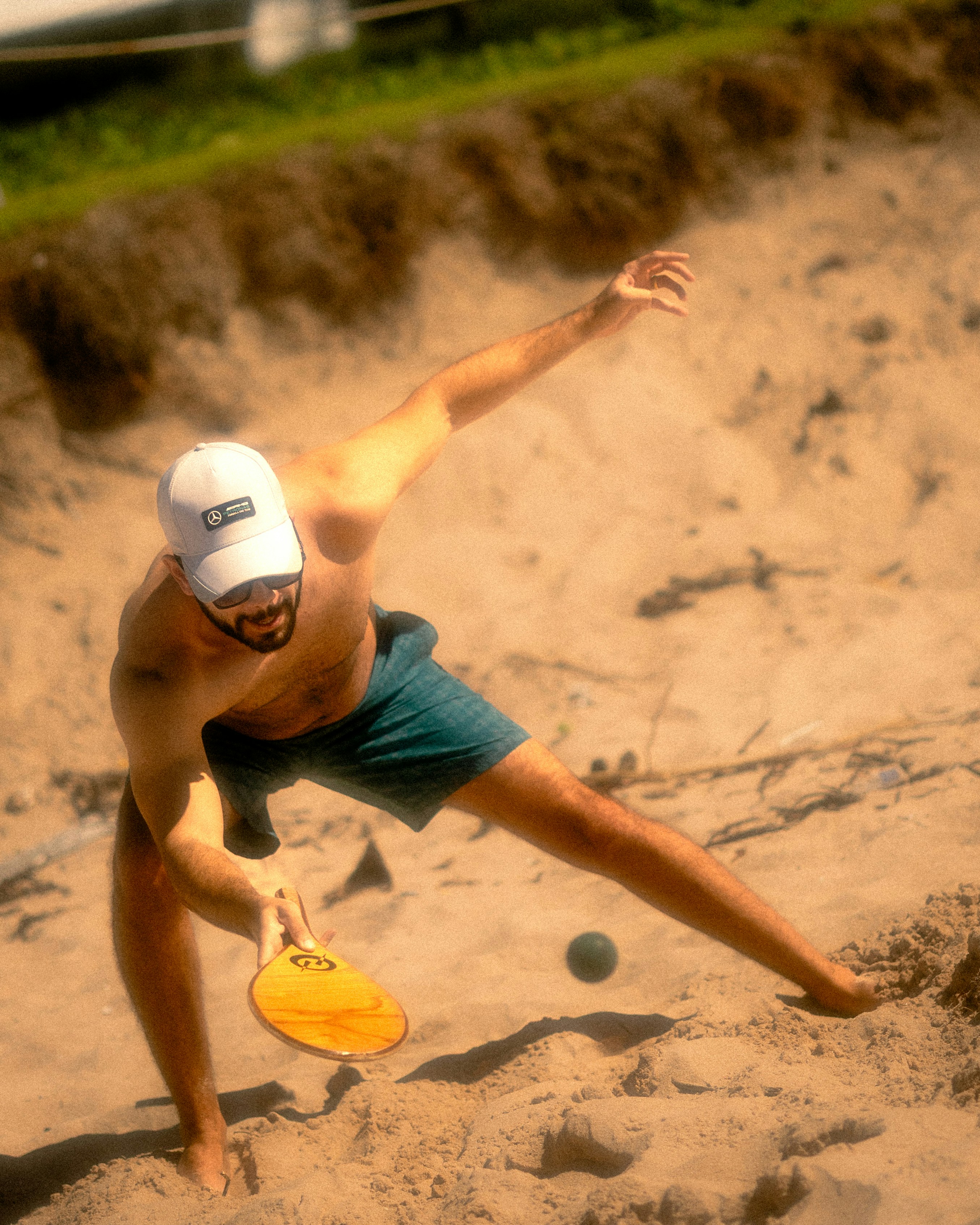 Dusty Beach Dash: A Shirtless Paddle Player Surging Across Sand