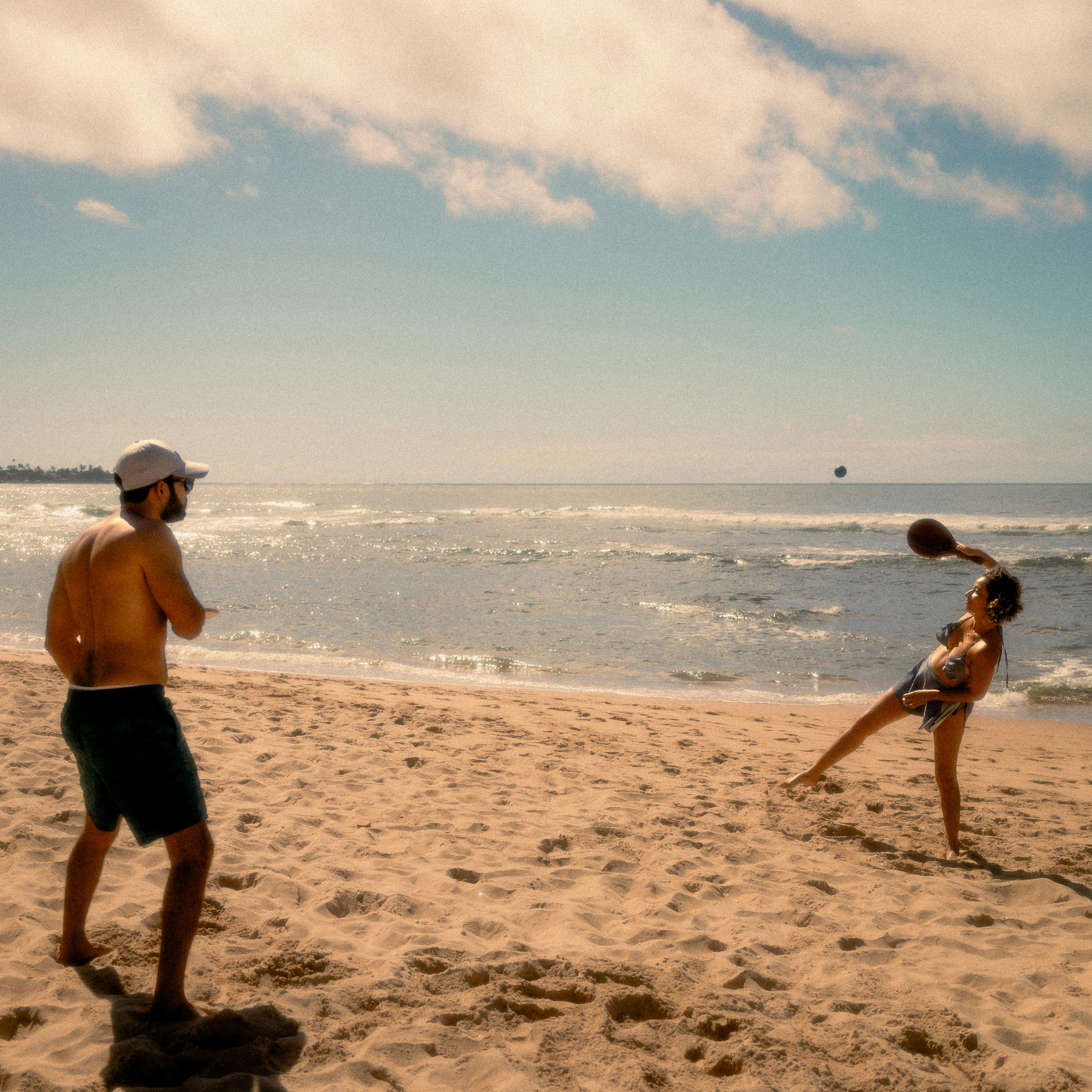 Two individuals enjoying a playful moment on the beach, with one preparing to throw a ball while the other watches attentively.