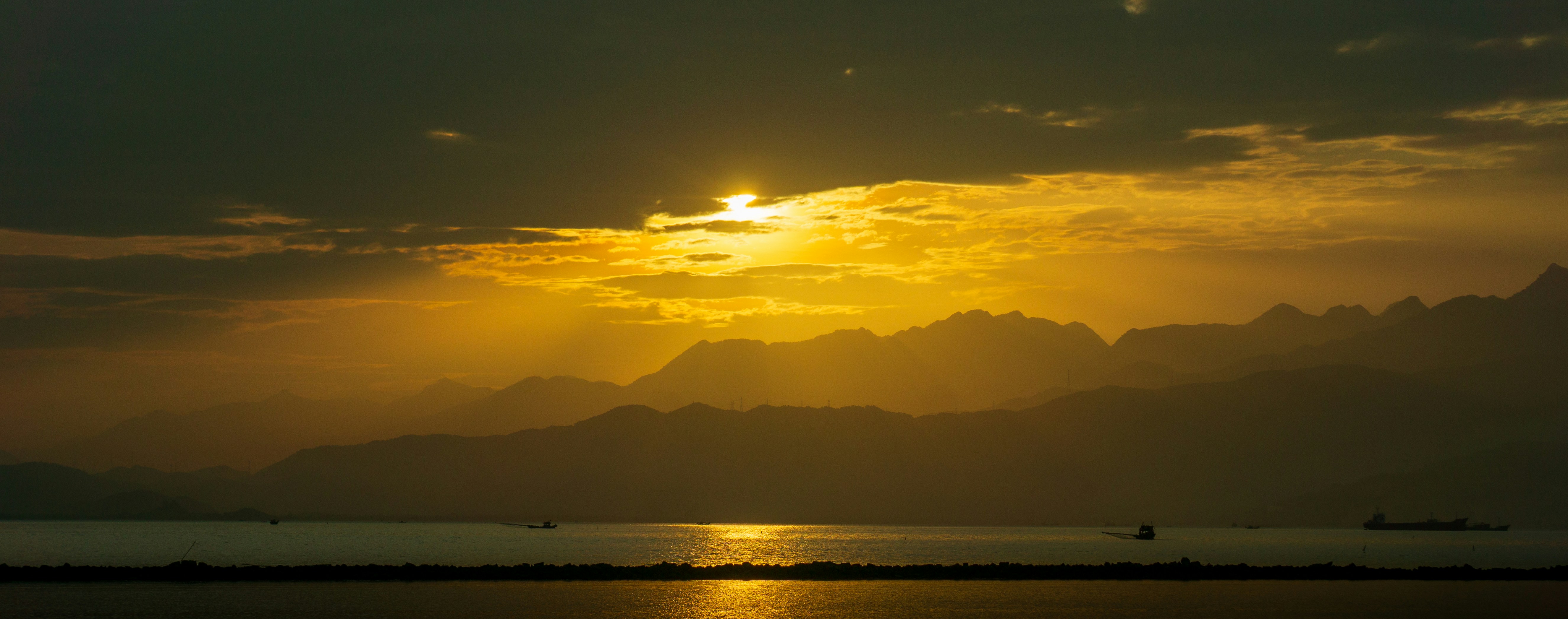 Sun and Beach | Golden sunset over hazy mountains and calm water