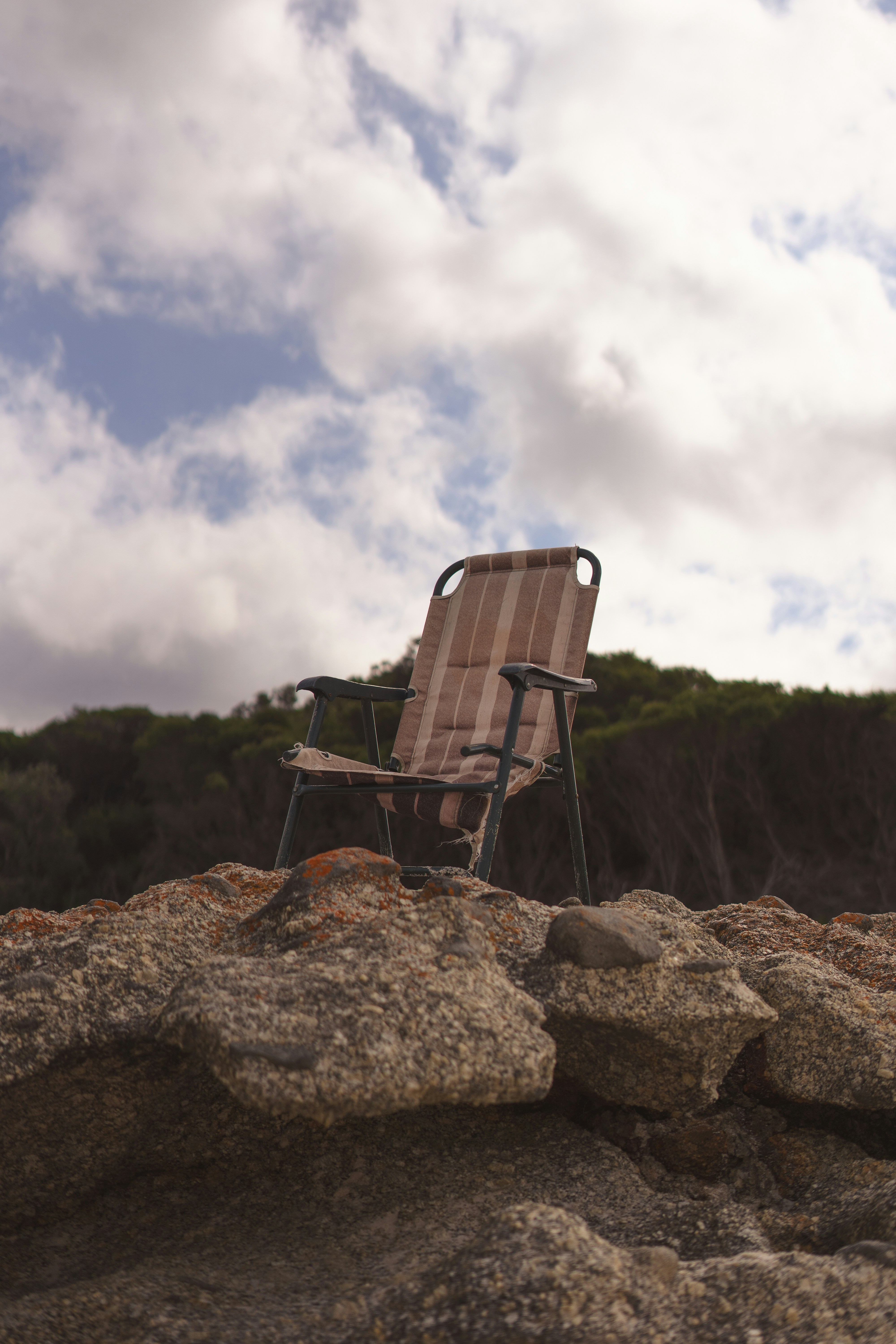 A striped chair sits on rocks by the sea.