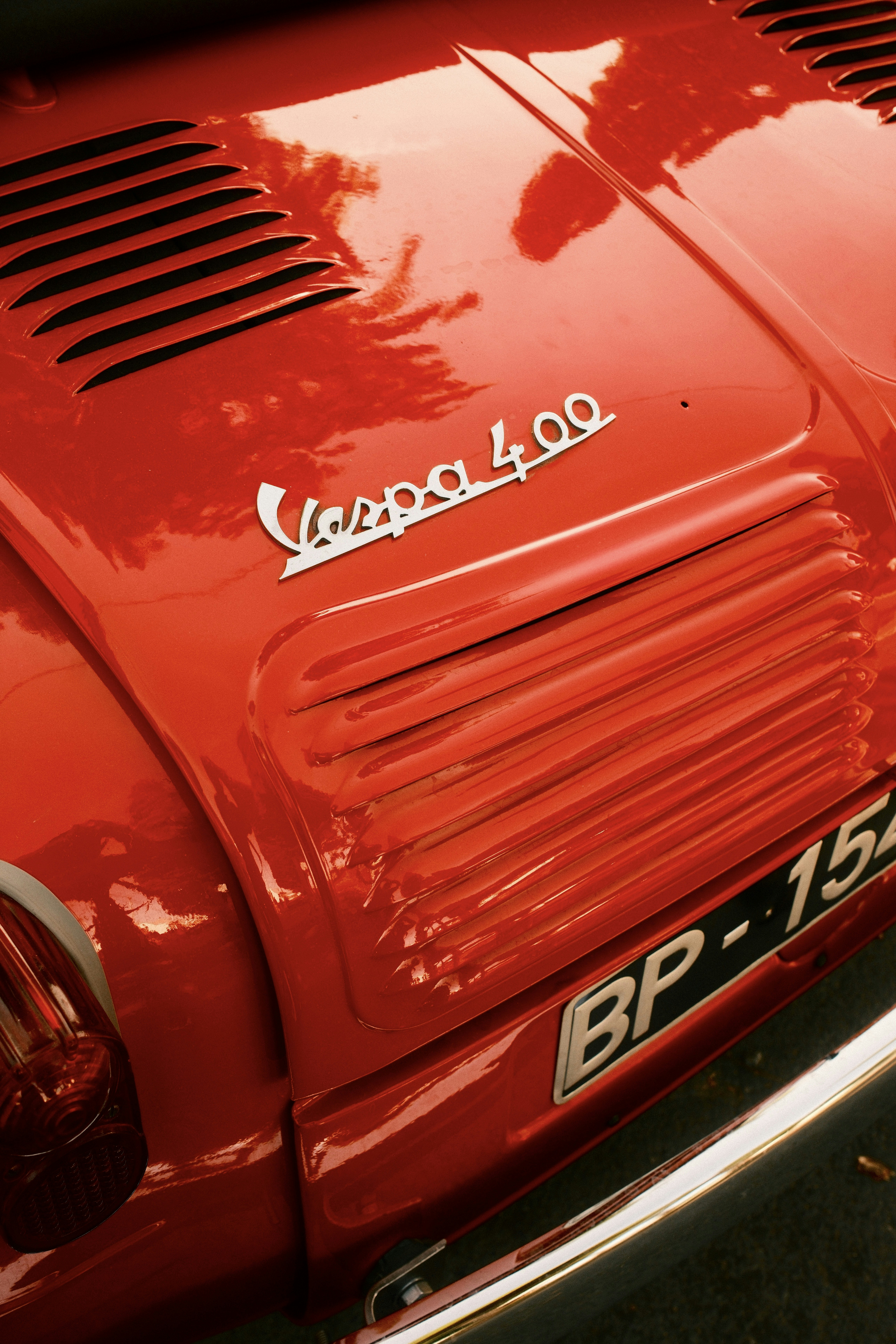 A charming Vespa 400, a tiny jewel from 1957, resting quietly on the streets of Nantes — a timeless whisper of vintage elegance. | Close-up of a shiny red vespa 400 car trunk.