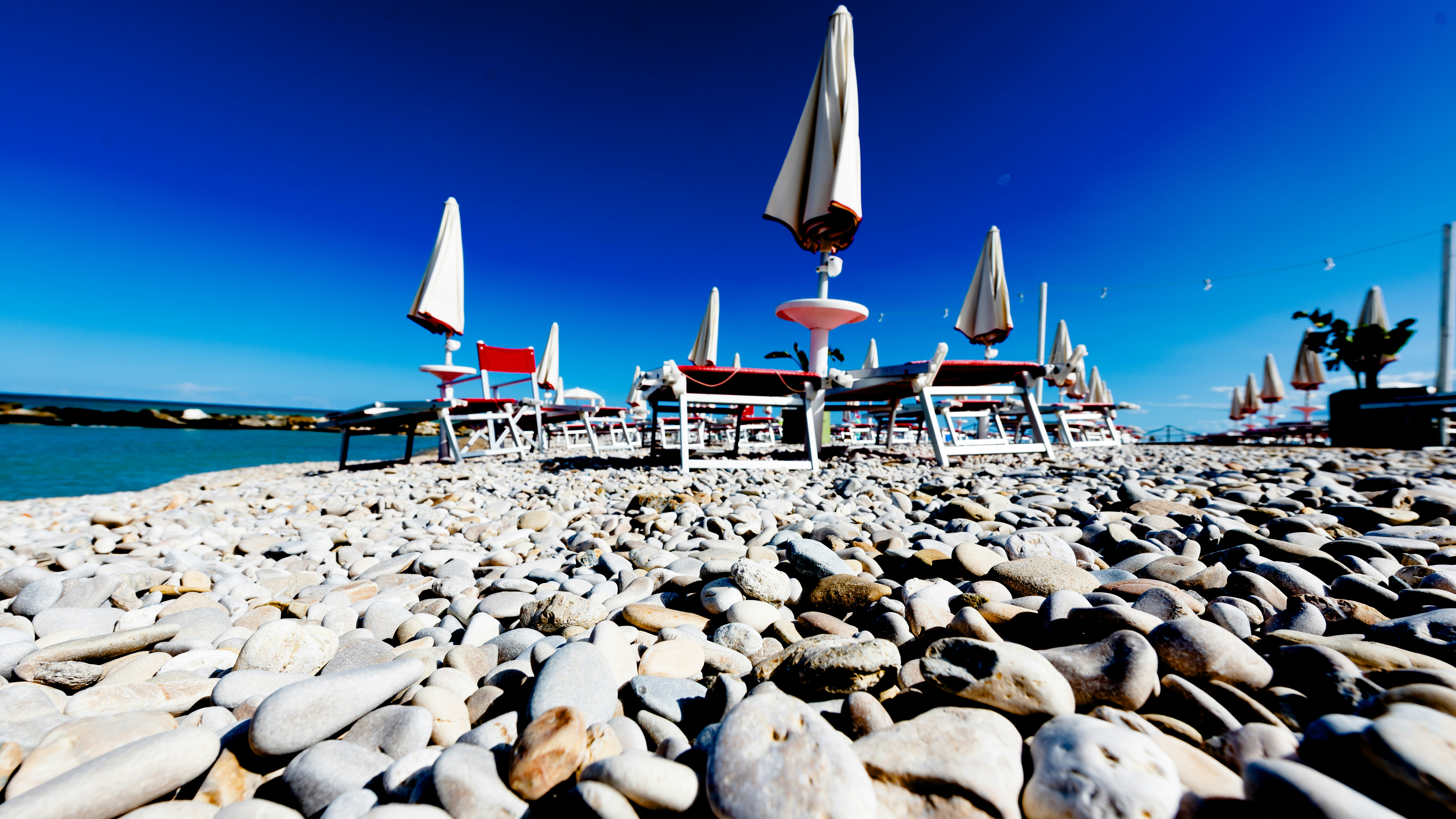 Pebble Beach Parade: Red Loungers and White Umbrellas Framing a Calm Sea