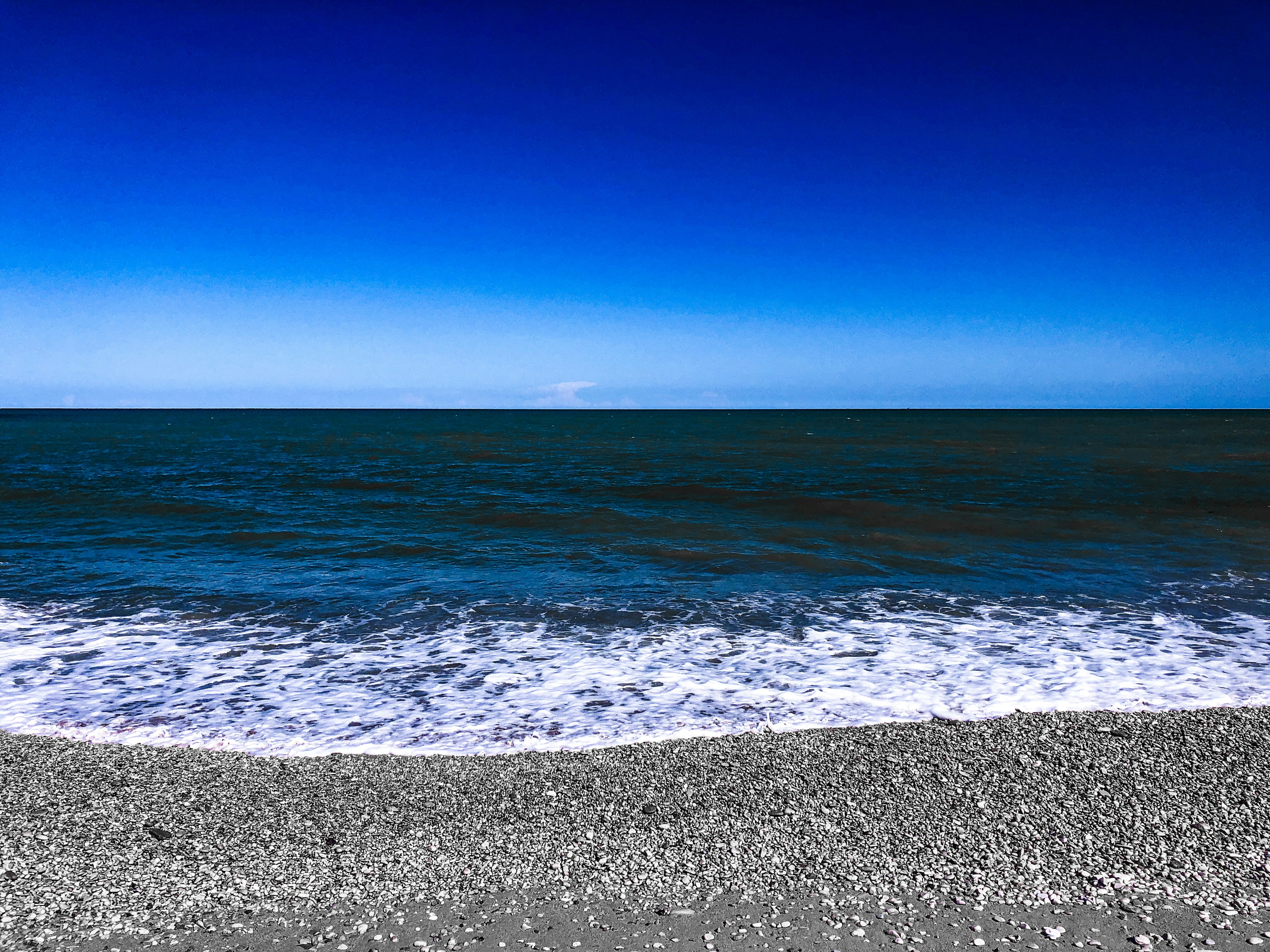 AsMainTitle | Ocean waves crash on a pebble beach under blue sky