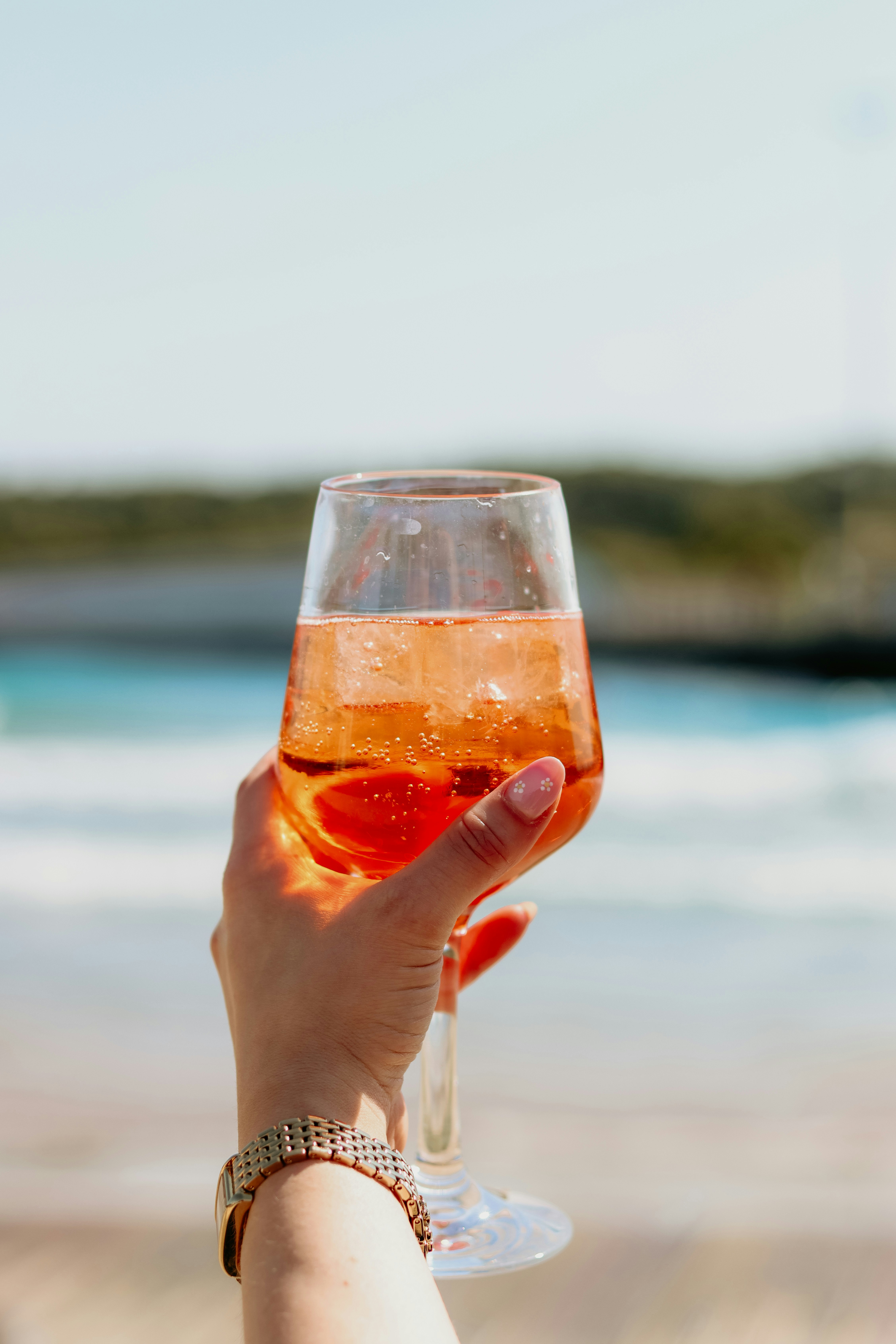 Hand holding a refreshing orange cocktail by the sea.