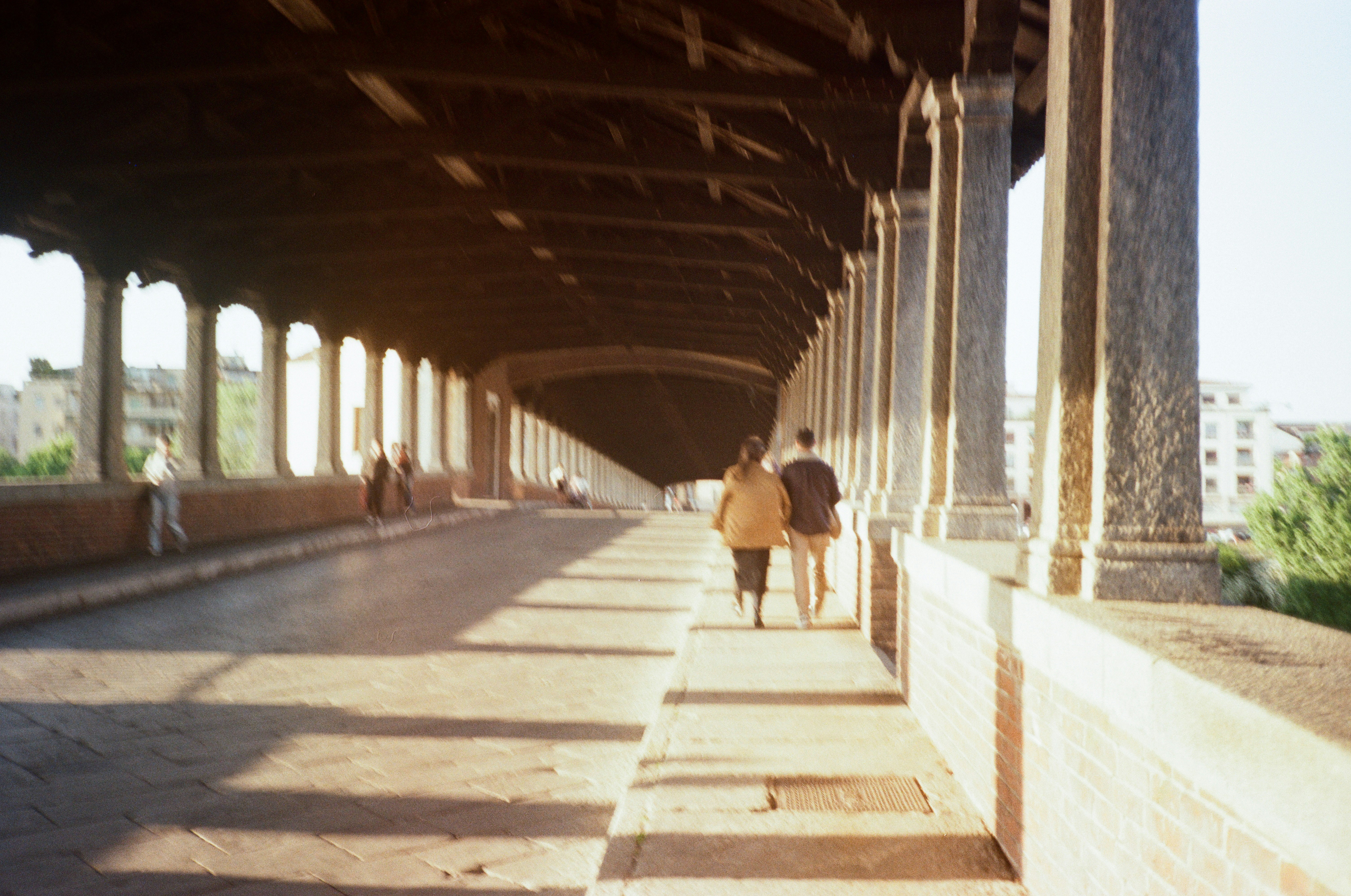 Couple walking on covered bridge with sunlit arches