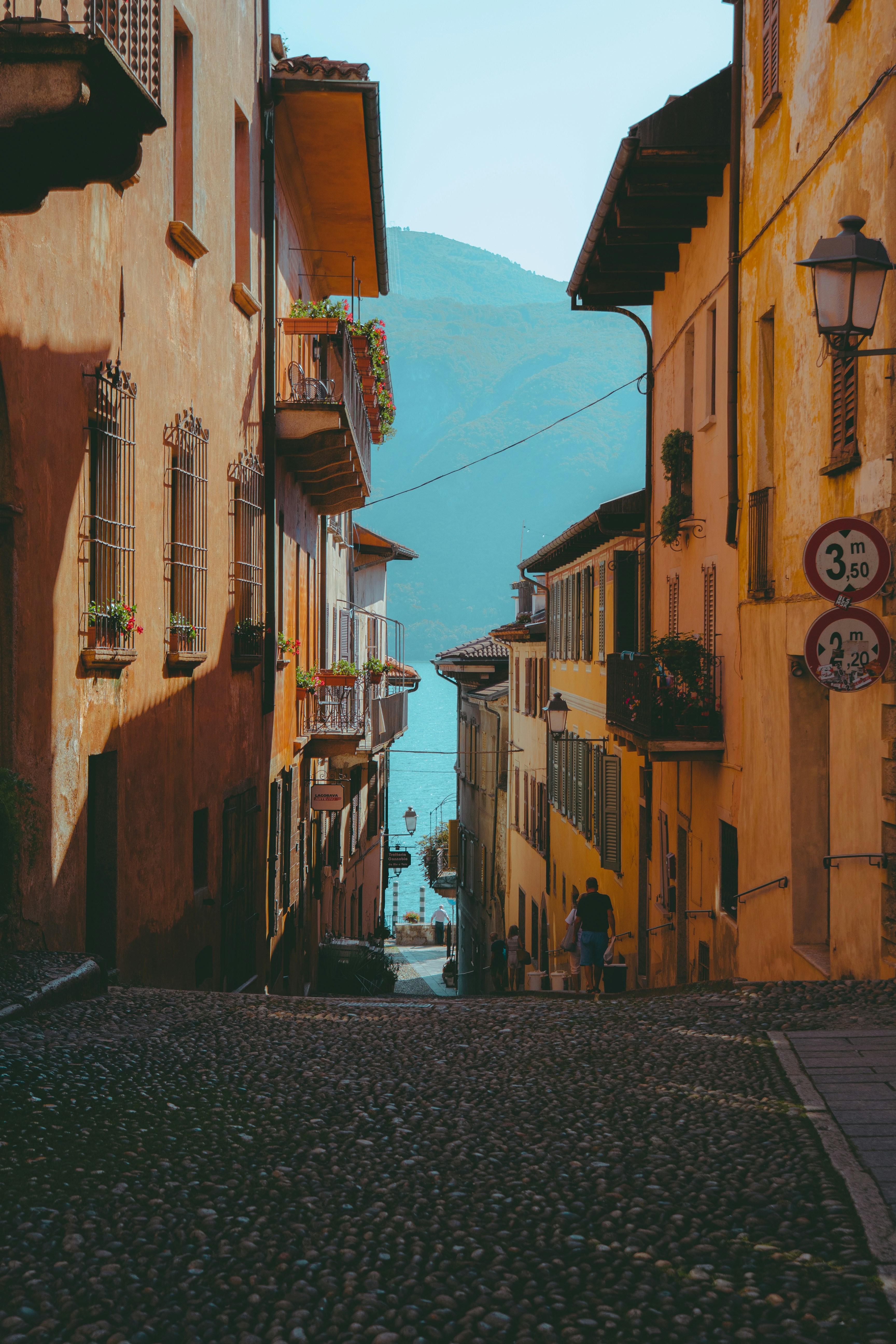 Narrow cobblestone street between colorful buildings leading to water.