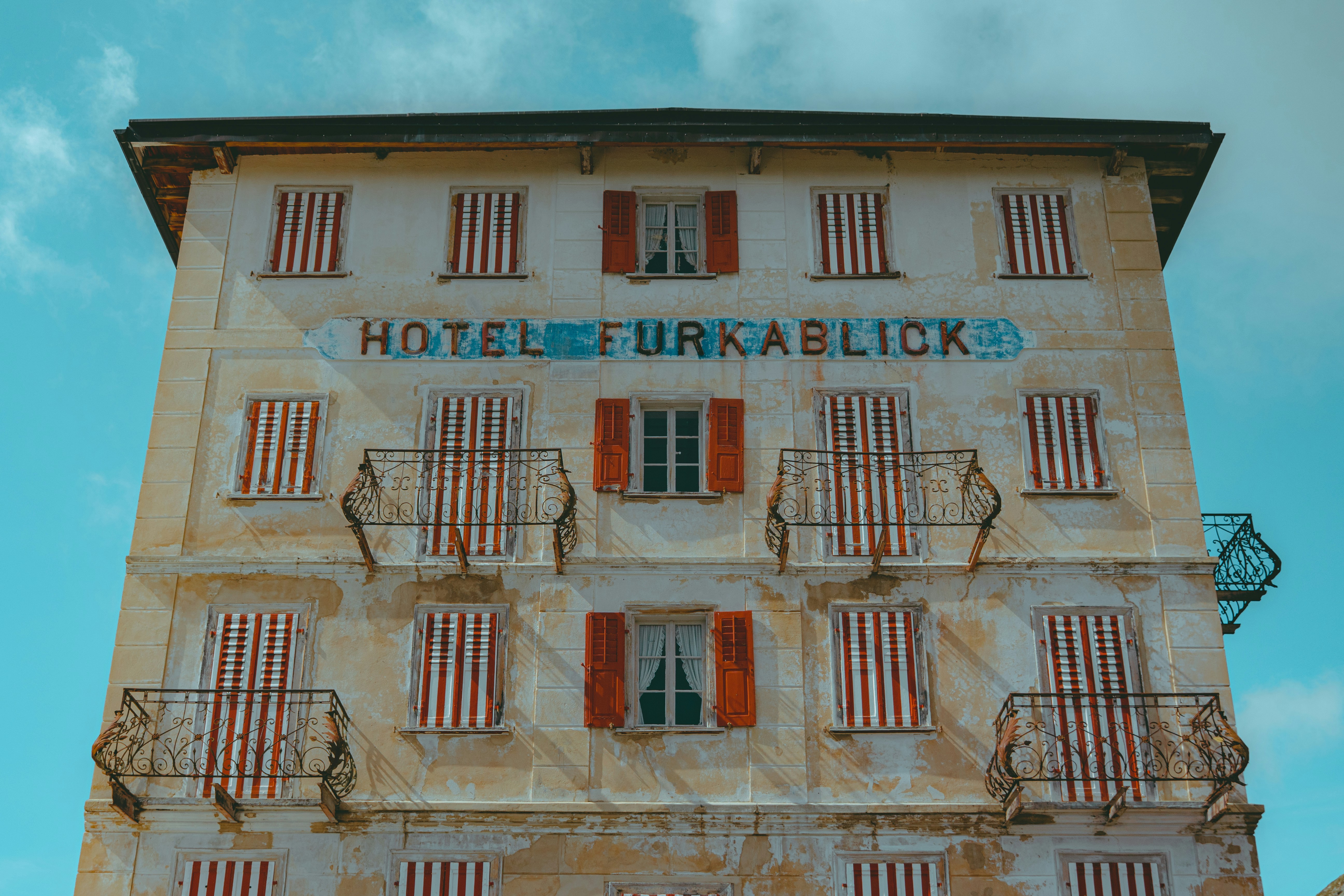 Historic hotel facade featuring vibrant red shutters and decorative balconies against a clear blue sky.