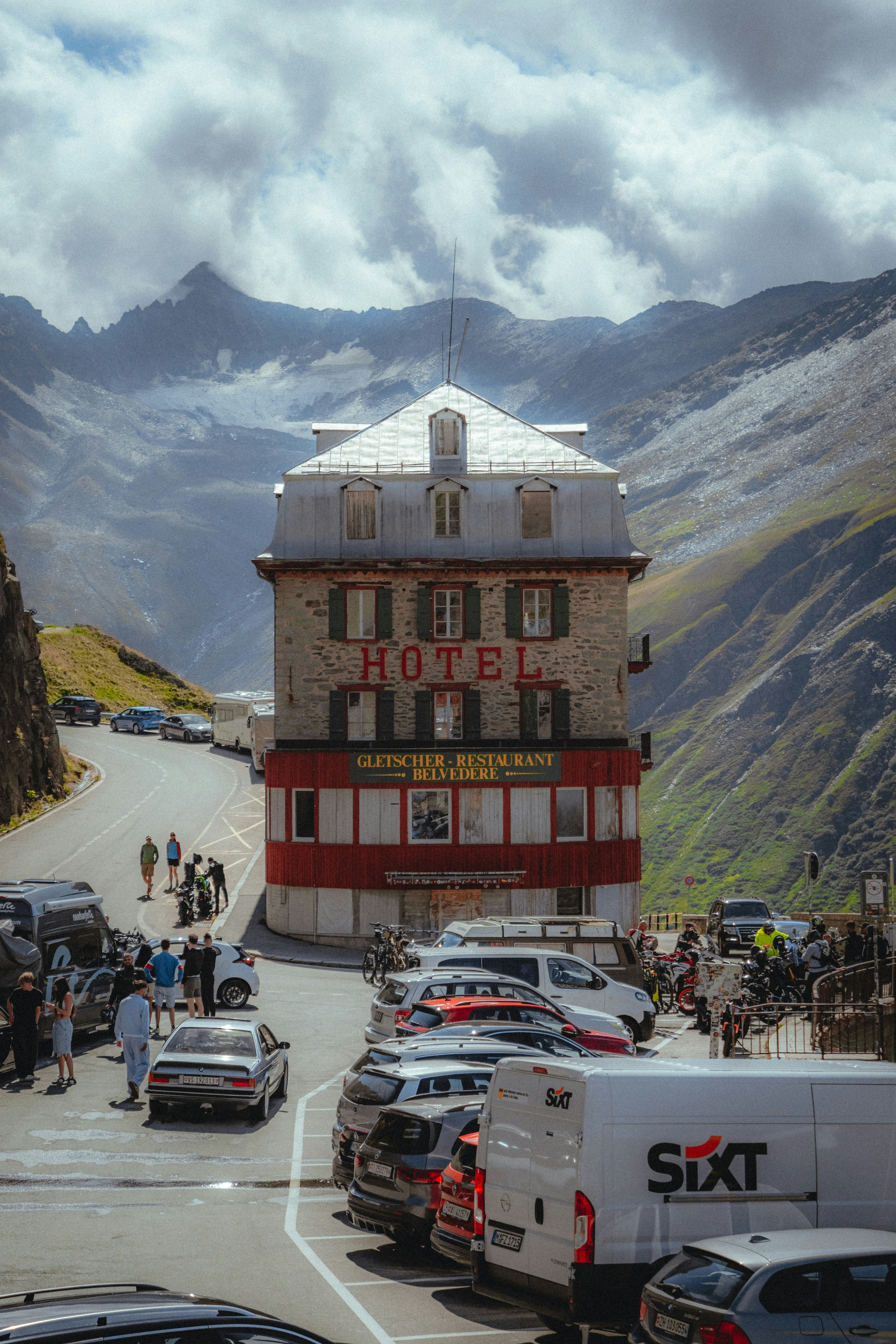 Historic hotel nestled in the mountains, surrounded by vehicles and visitors enjoying the scenic landscape. The building's architecture reflects a blend of rustic charm and modern allure.