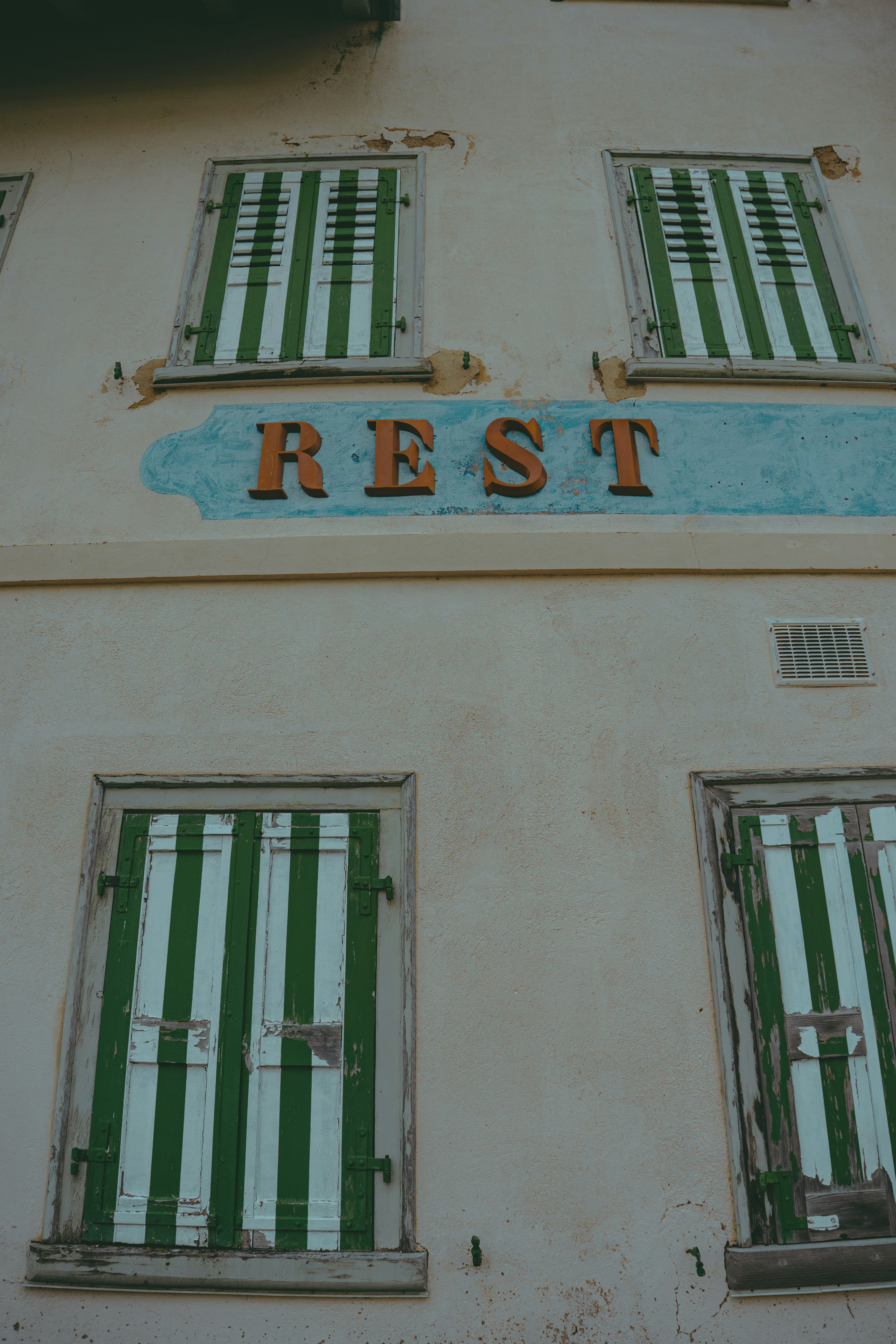 Building facade with striped shutters and "rest" sign.