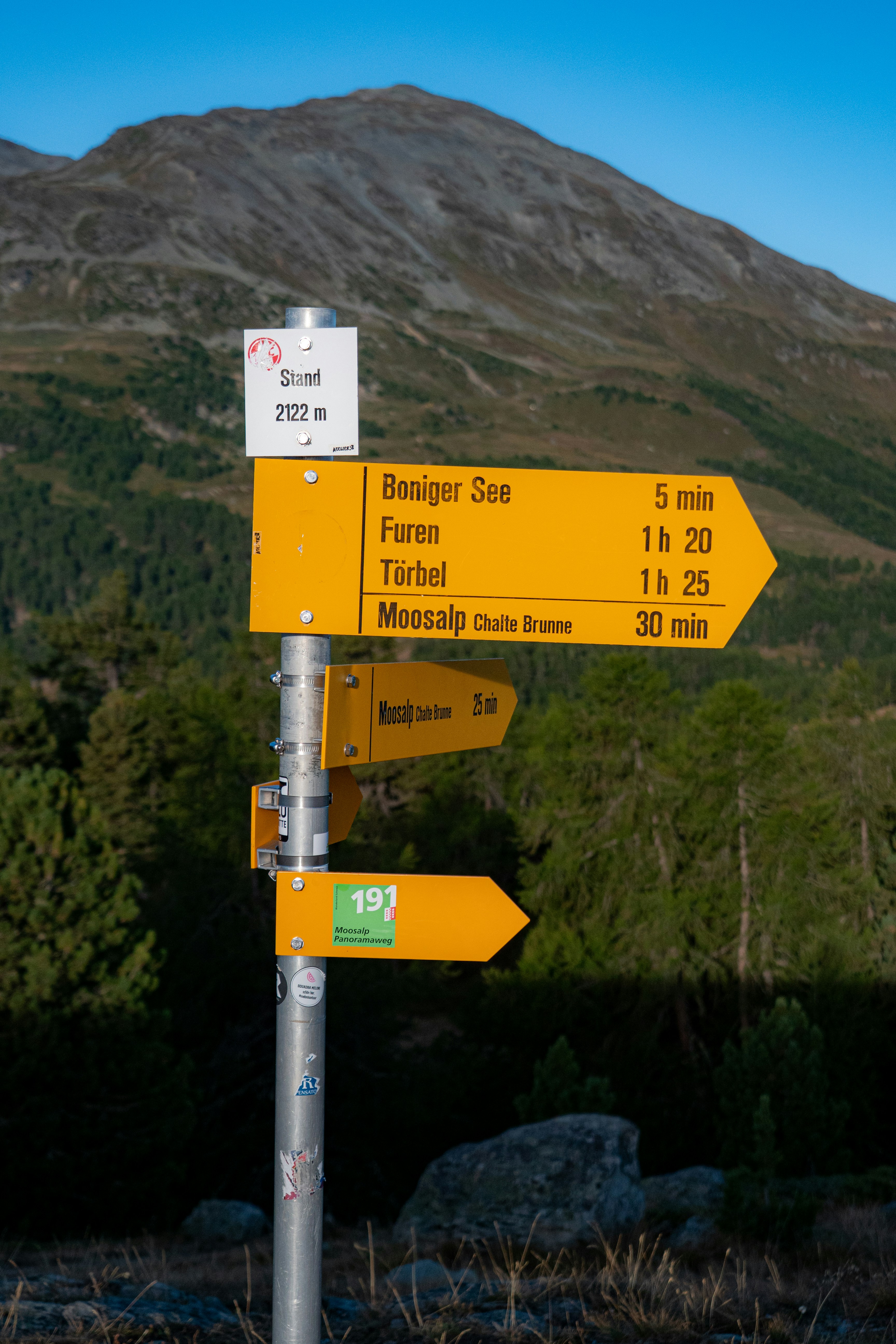 Directional signpost indicating hiking times to various destinations at an elevation of 2122 m, surrounded by mountainous terrain.