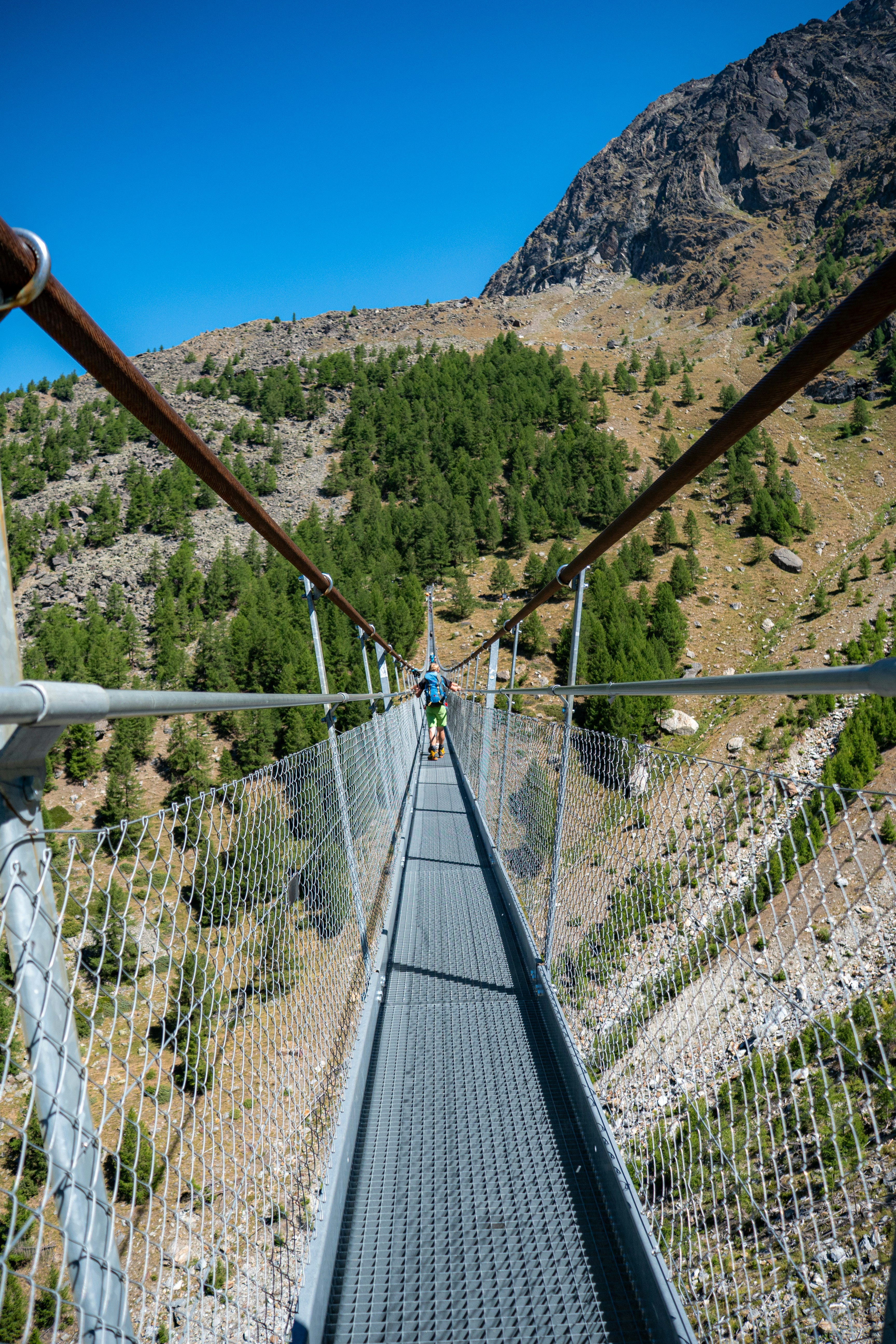 Person walking across a long suspension bridge in mountains.