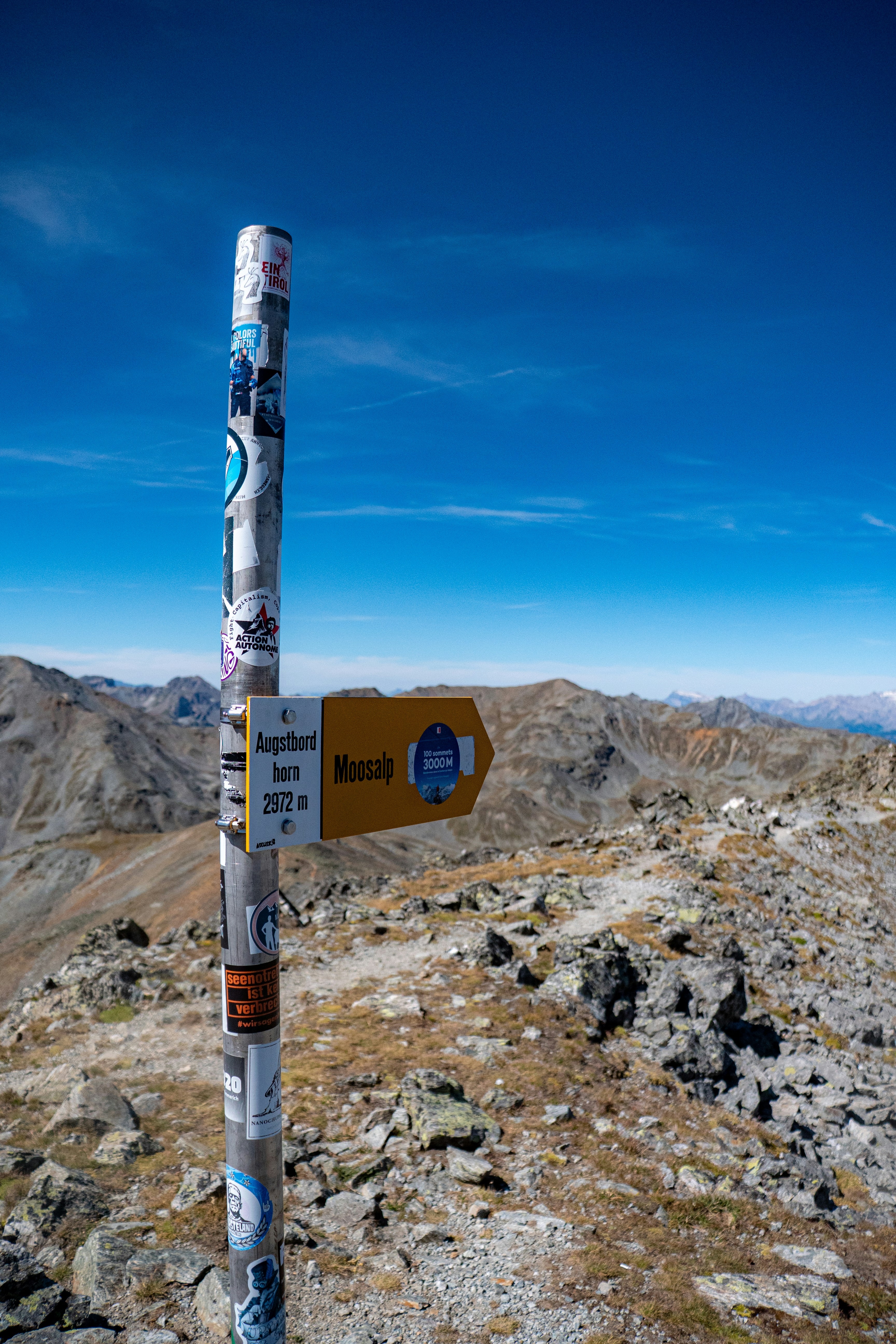 Stickered Summit Signpost Over a Rugged Alpine Rim
