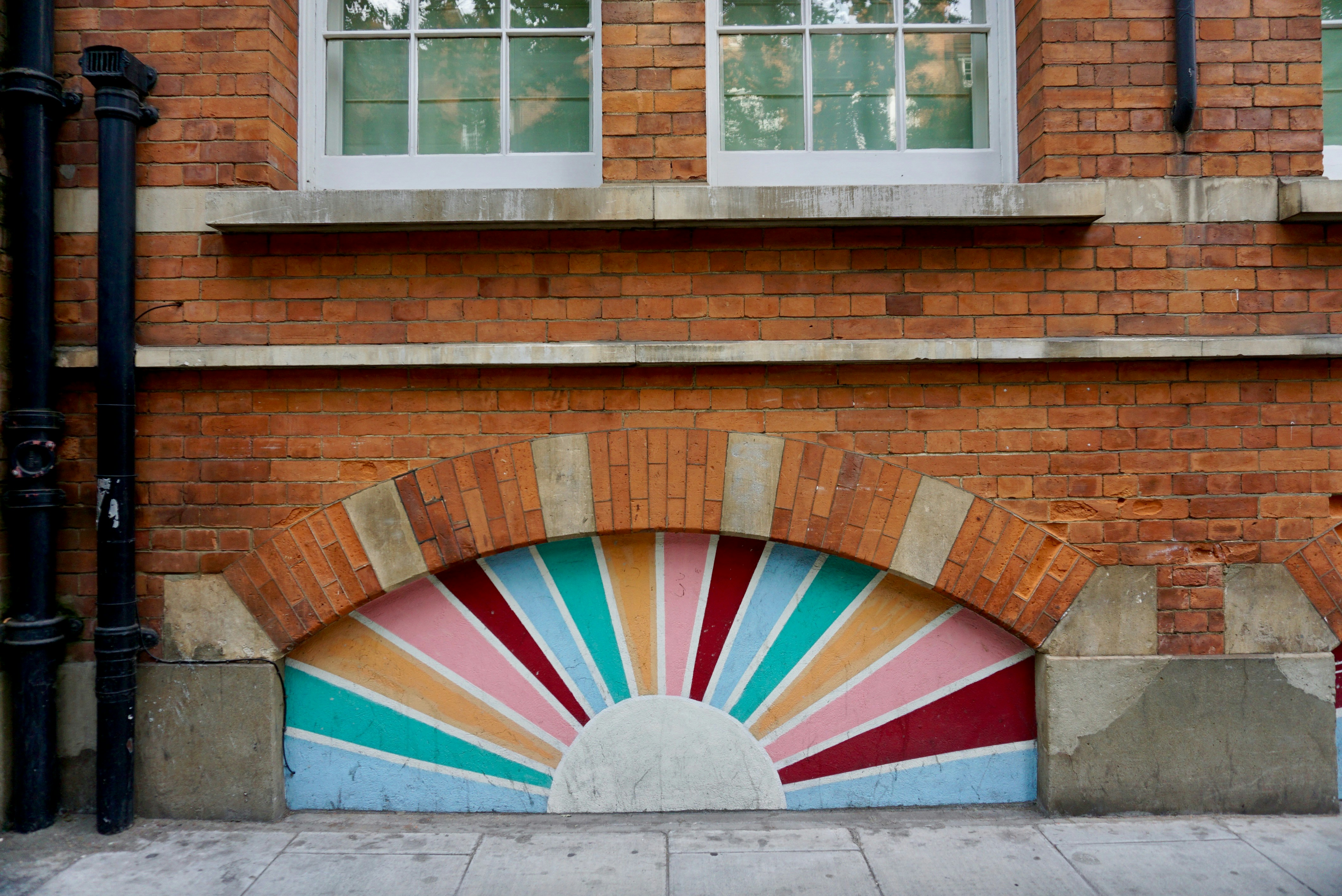 Colorful sunburst mural on brick building facade.
