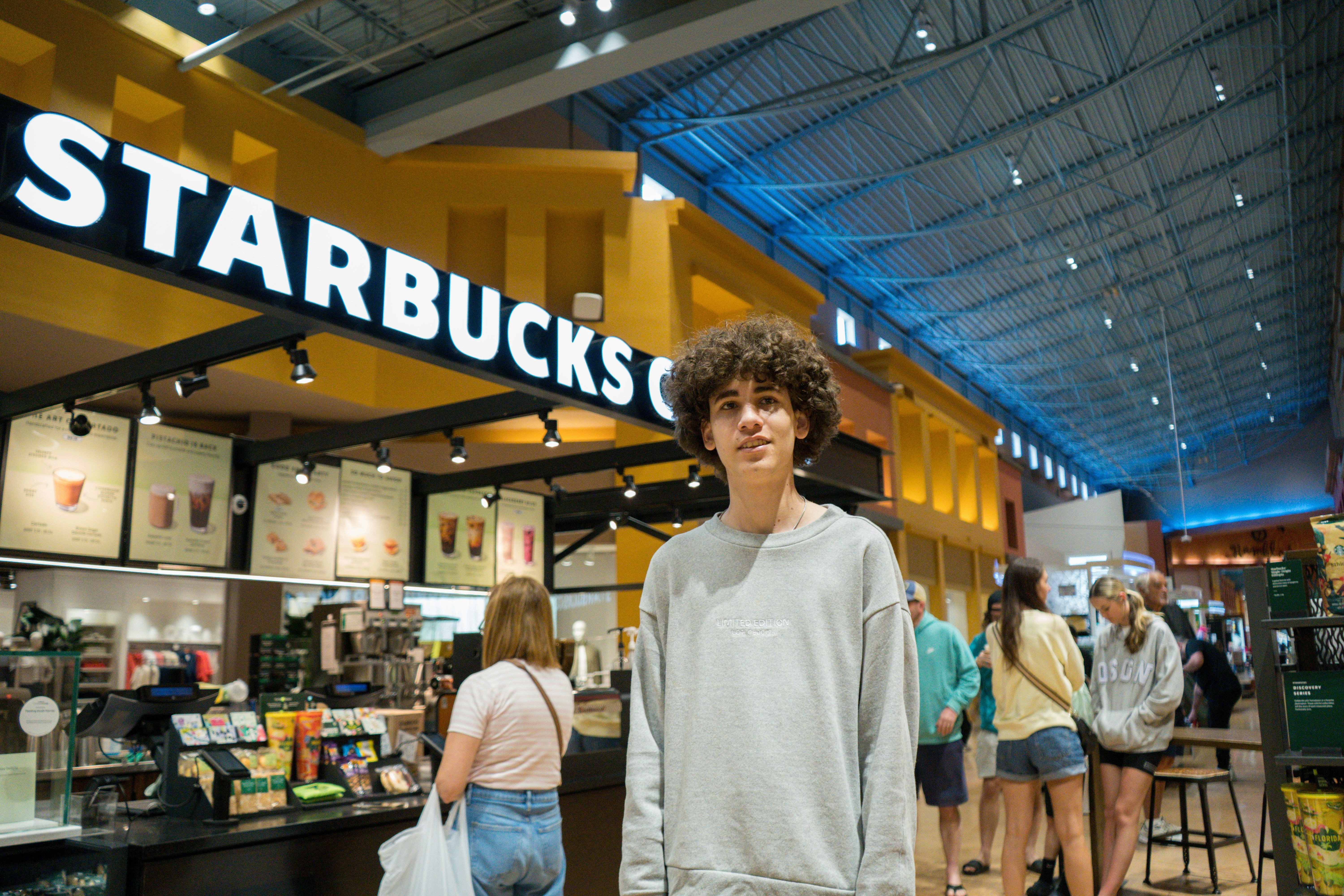 Center Frame: A Youth Stands Calm Amid Starbucks Buzz