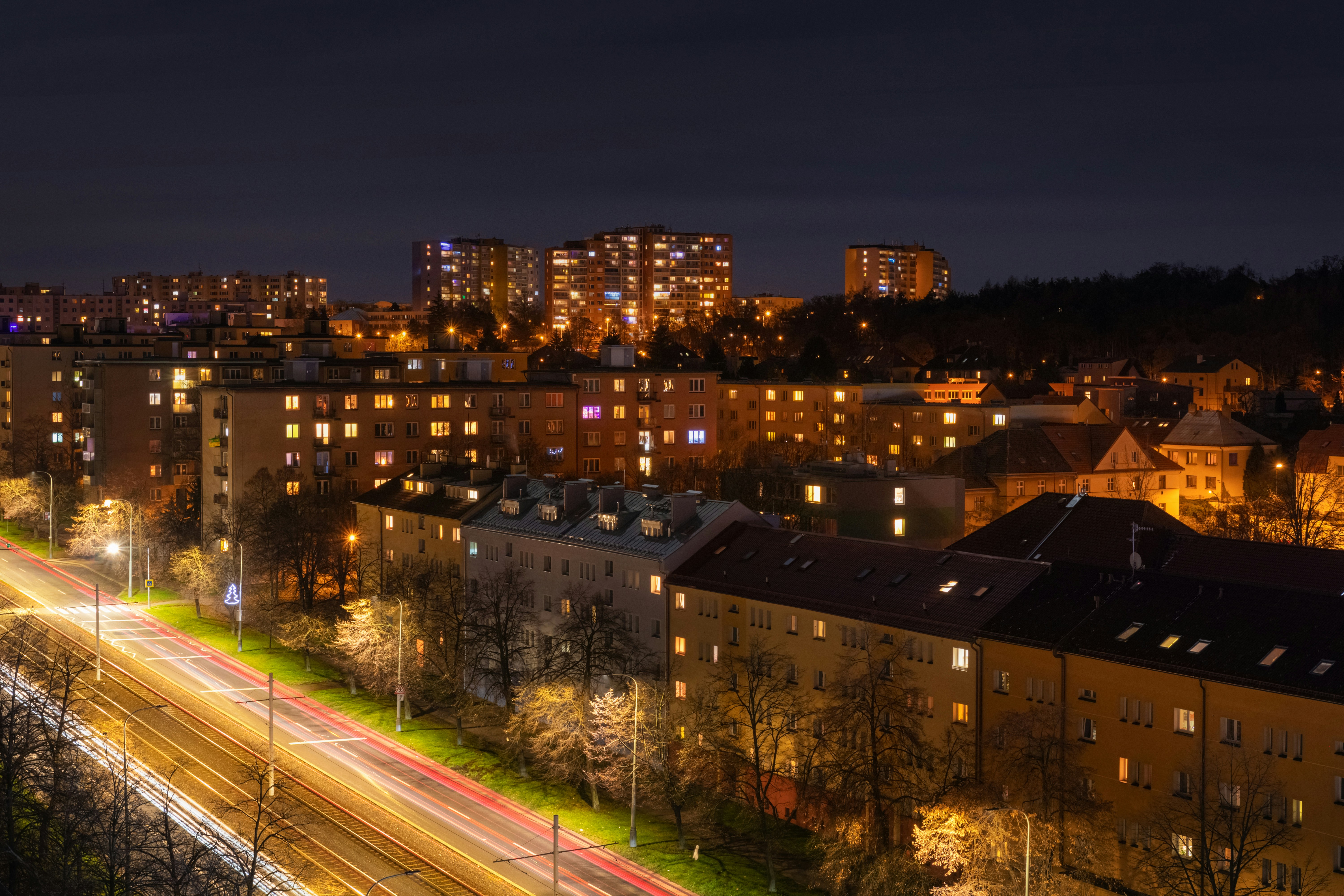 City buildings illuminated at night with light trails on road.