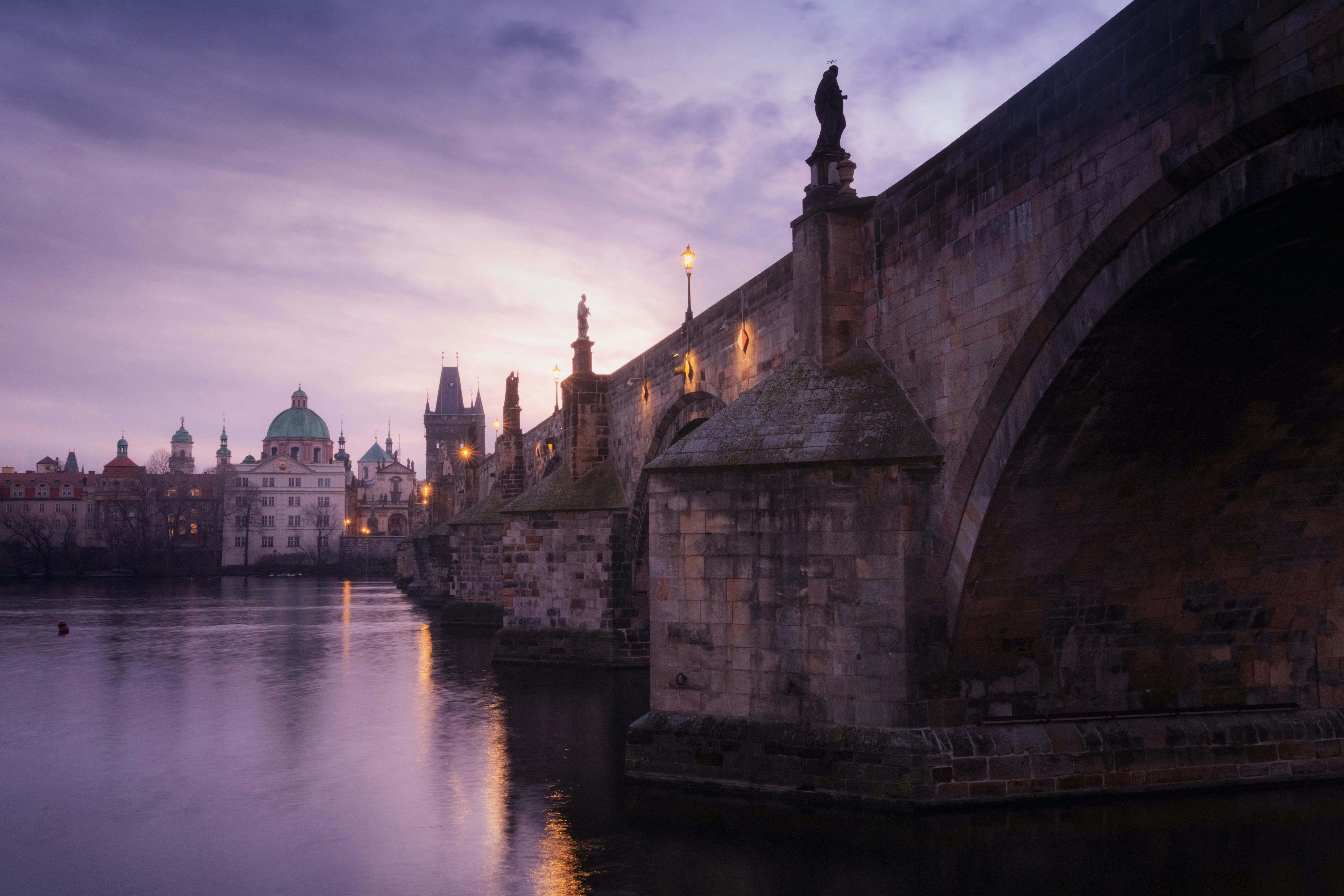 Stone bridge with statues over river at dusk