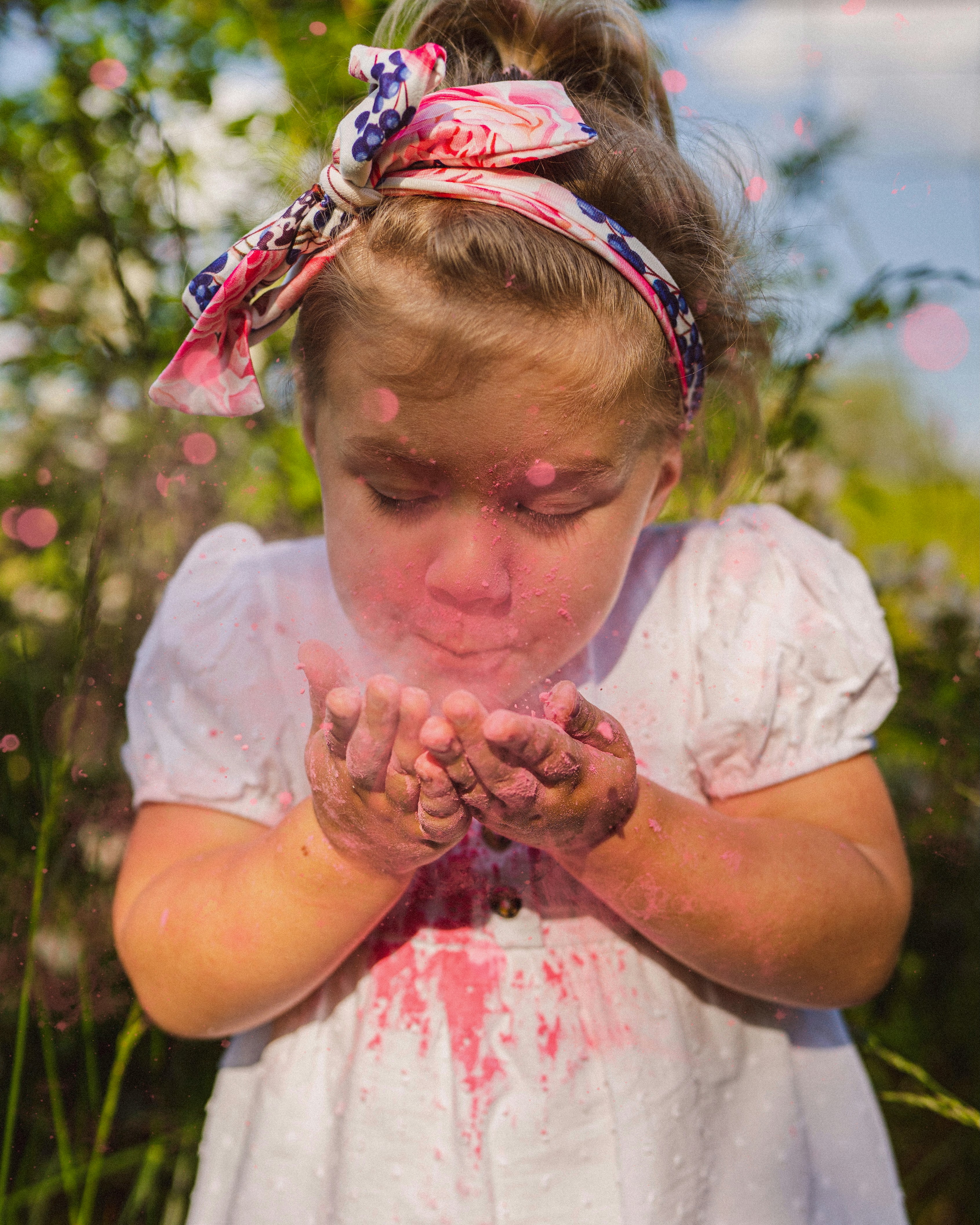 A young girl blowing pink powder from her hands