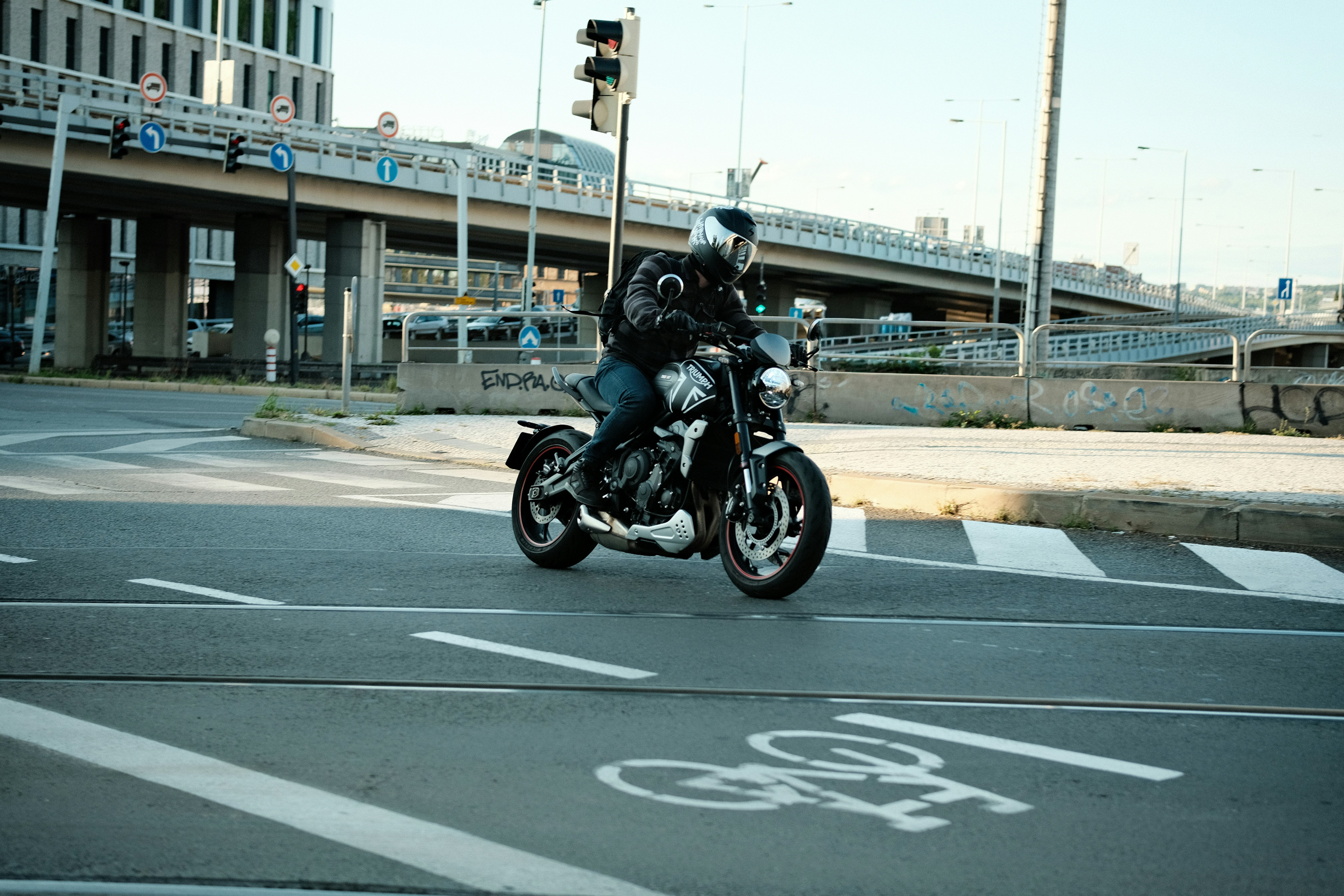 Motorcyclist riding on urban street near bridge | Man riding motorcycle on city street with bike lane.