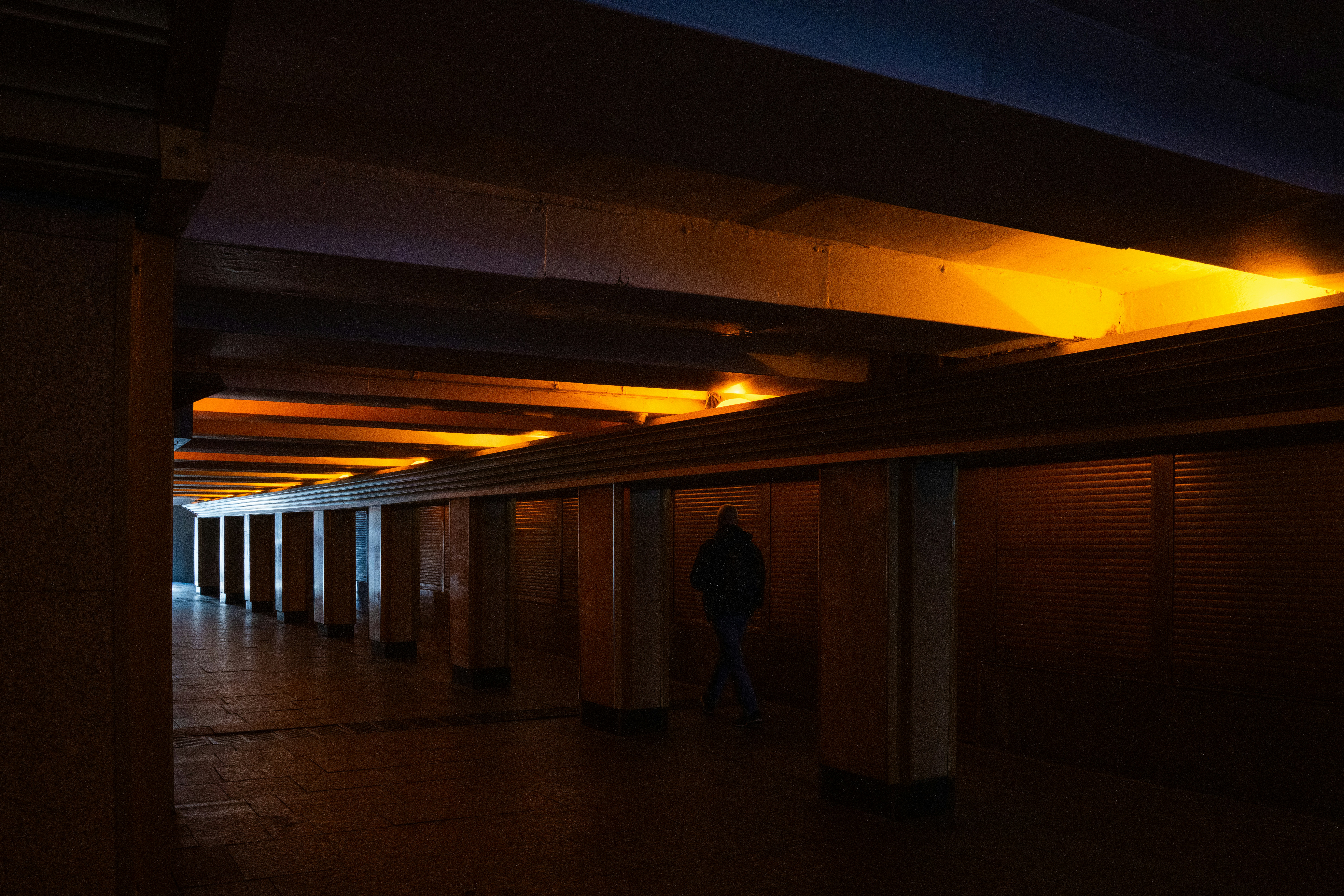 A lone figure walks down a dimly lit underpass.