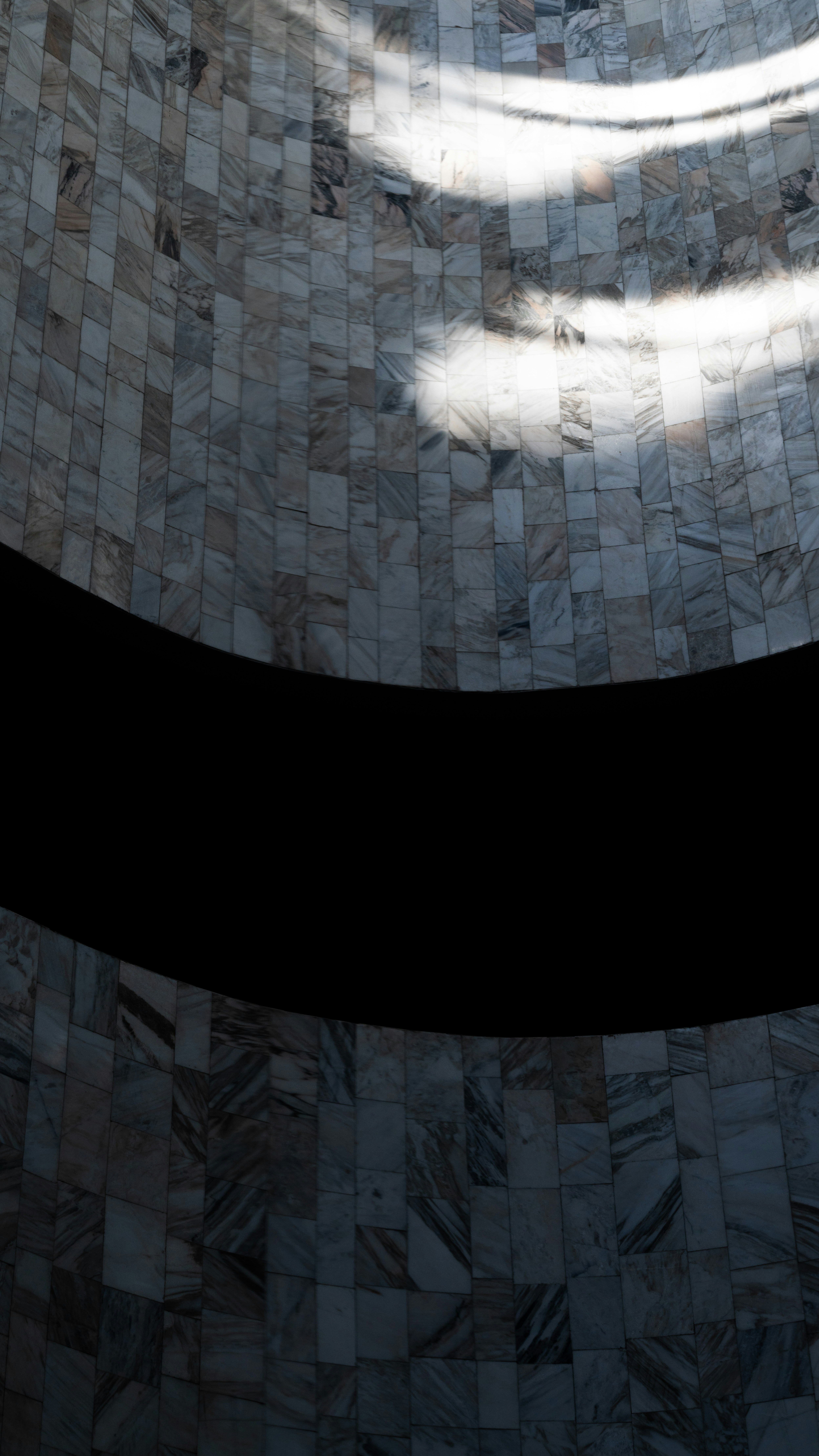 Light reflects off polished marble tiles, creating an abstract interplay of shadows and highlights. The dark curve contrasts with the textured surface below.