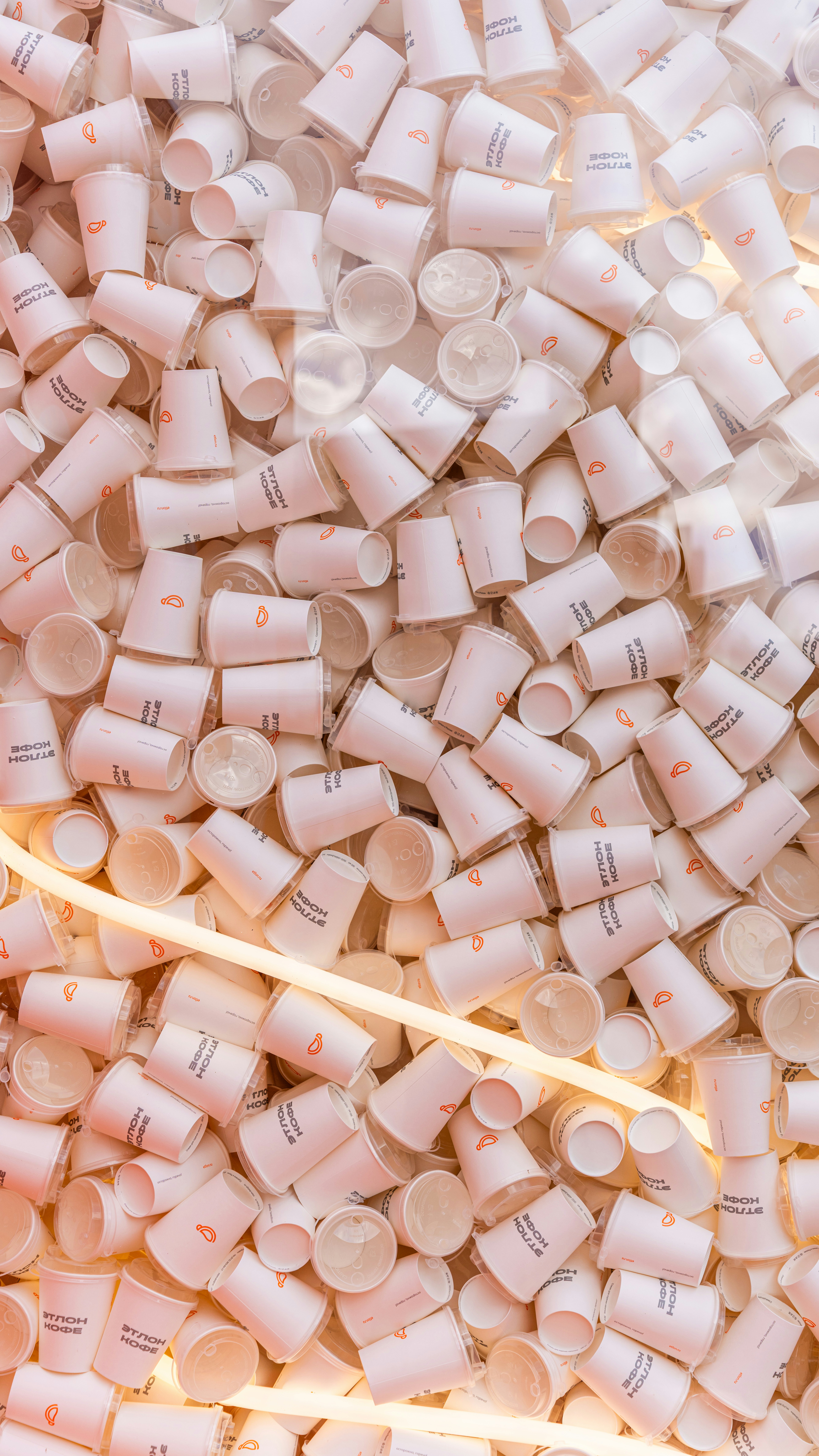 Pile of small white paper cups with orange logo.