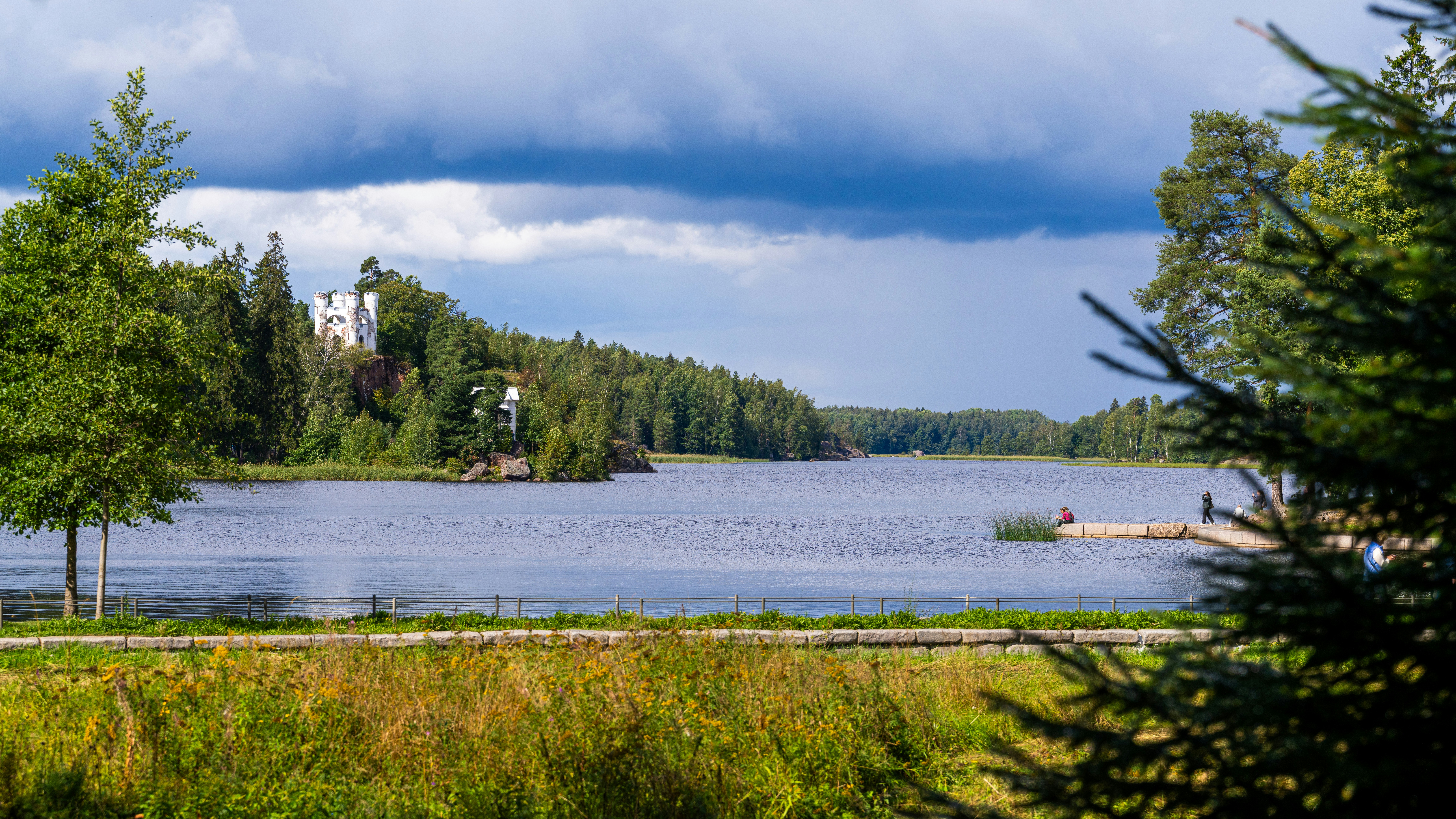 Serene lakeside view featuring lush greenery and distant structures under a cloudy sky. The scene captures the essence of peaceful nature.