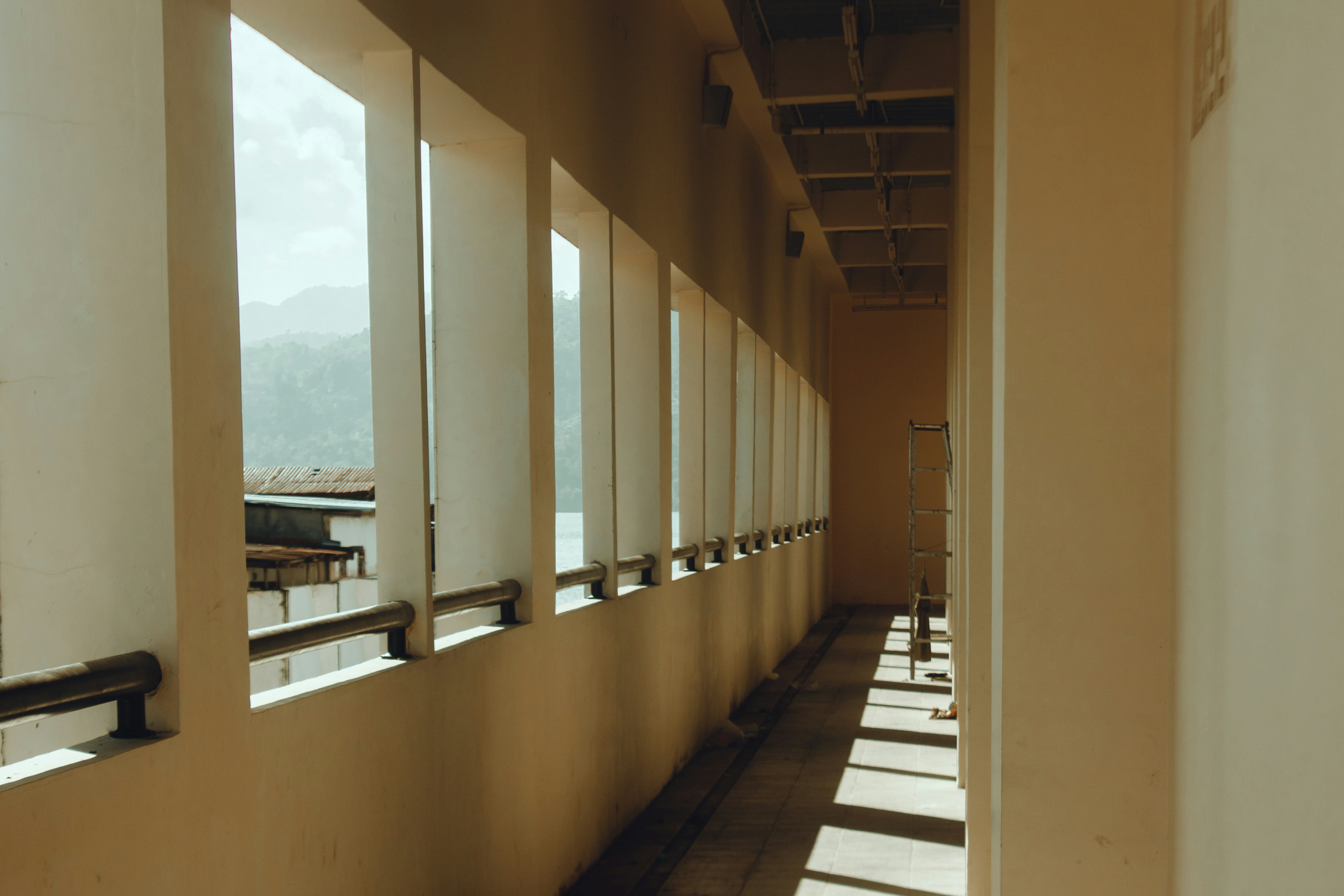 The building's hallways and window openings are rectangular. | Hallway with windows and sunlight casting shadows
