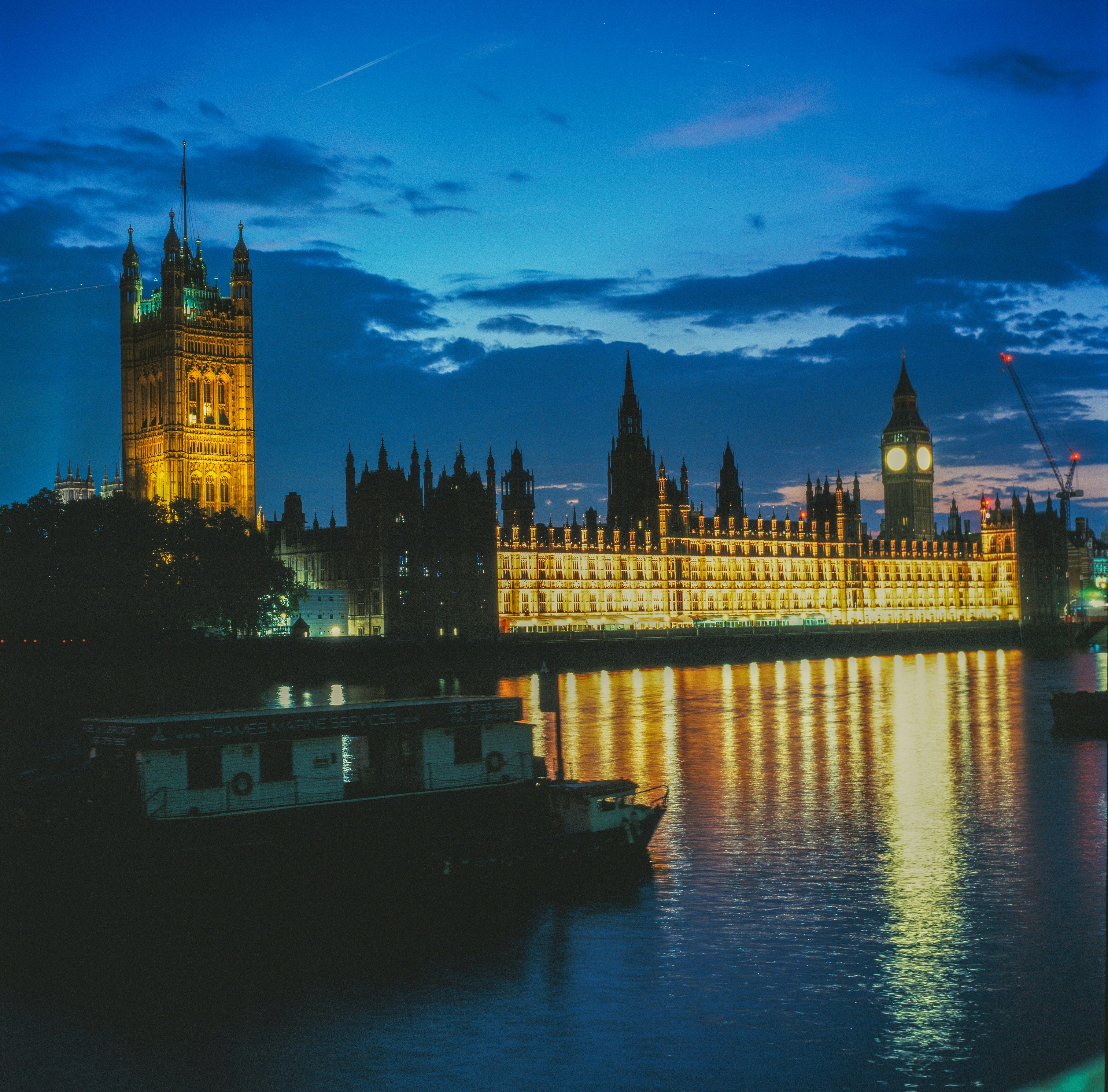 Illuminated Houses of Parliament and Big Ben reflected in the River Thames during twilight, with a serene sky transitioning from day to night.