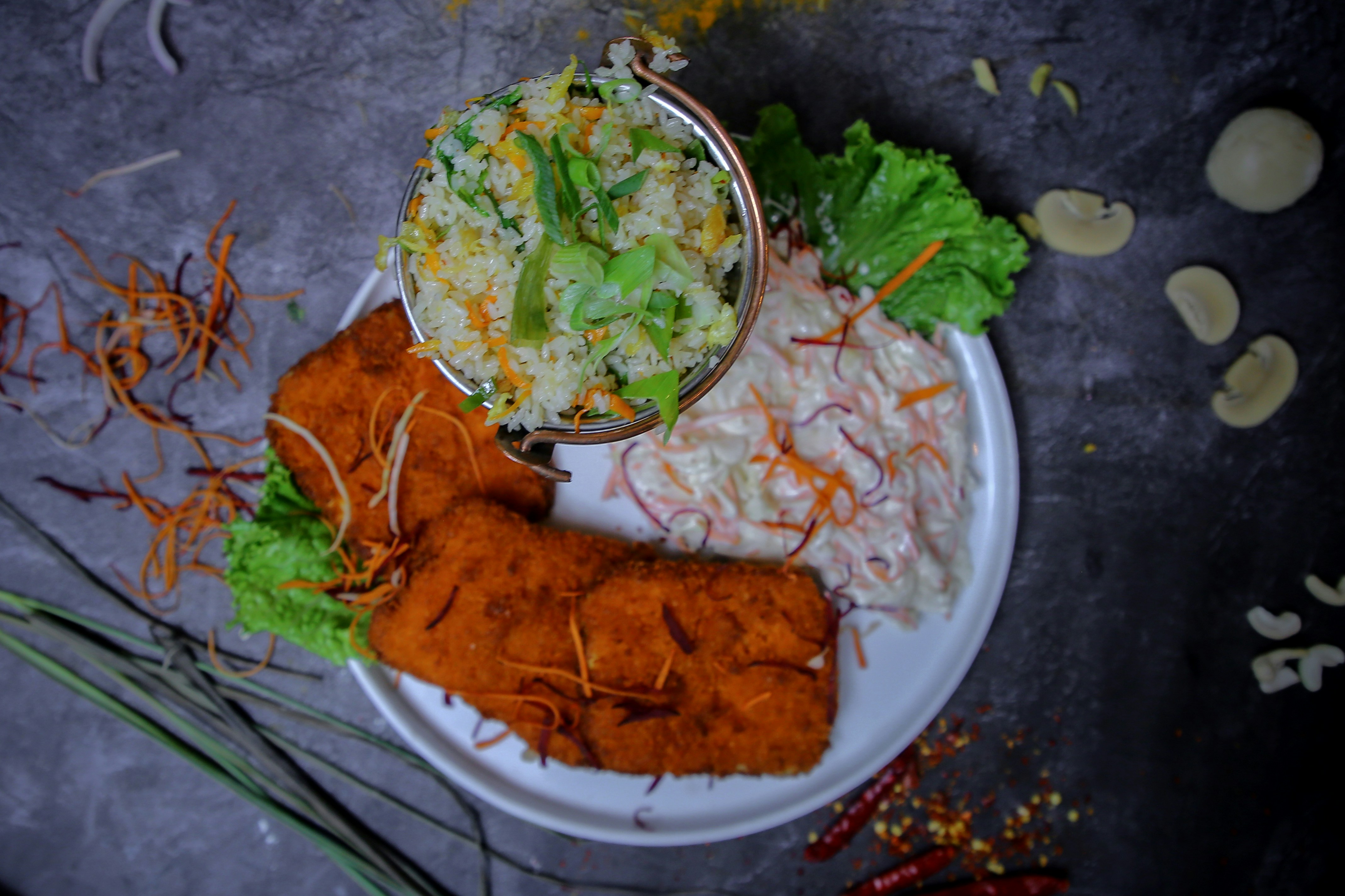 A vibrant plate featuring crispy fried fish, fresh salad, and aromatic rice garnished with herbs and spices. The composition highlights the colorful ingredients beautifully.