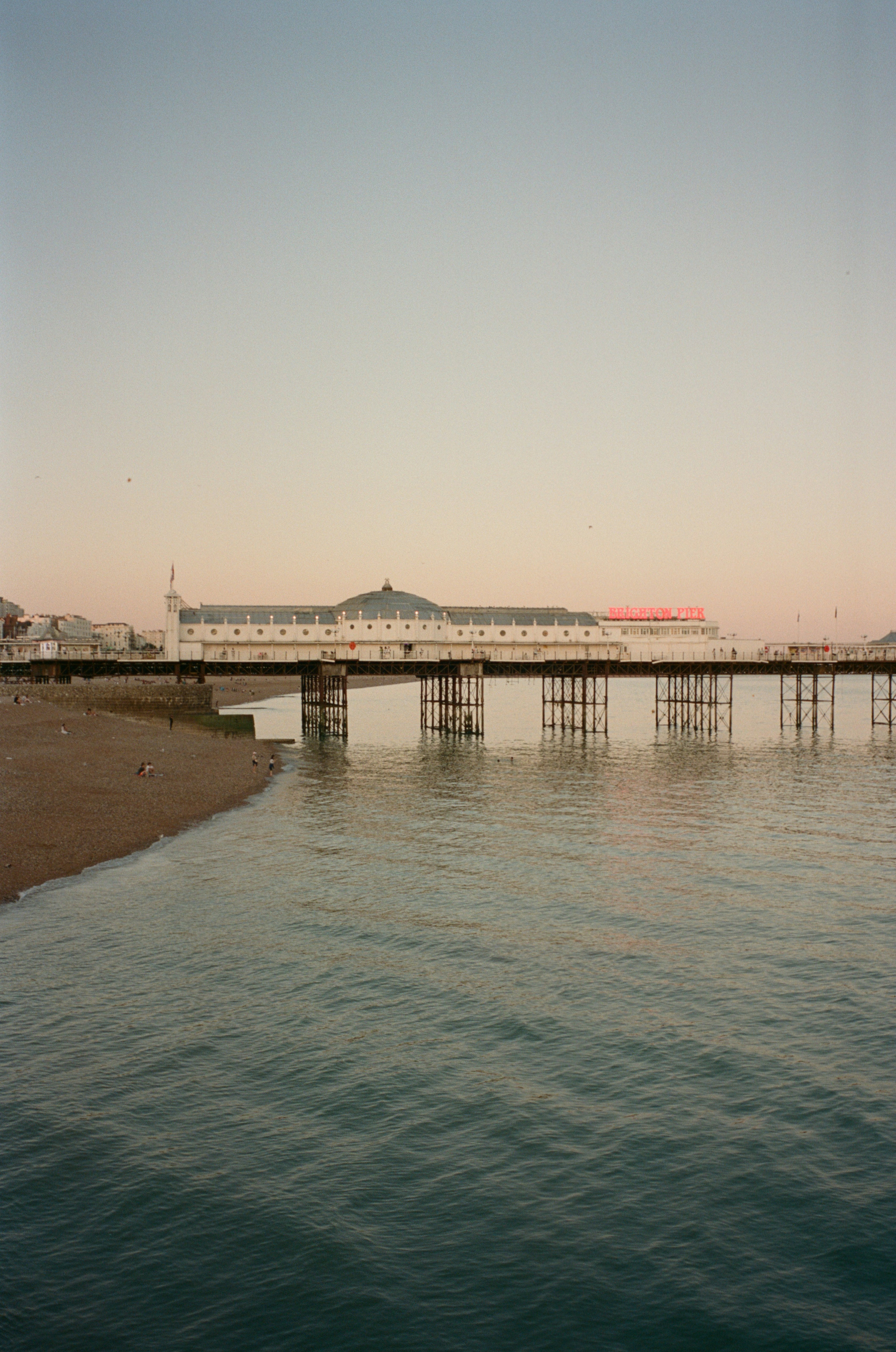 Historic pier extending over calm waters at dusk, with soft pastel hues in the sky. The structure showcases architectural details against a tranquil seaside backdrop.