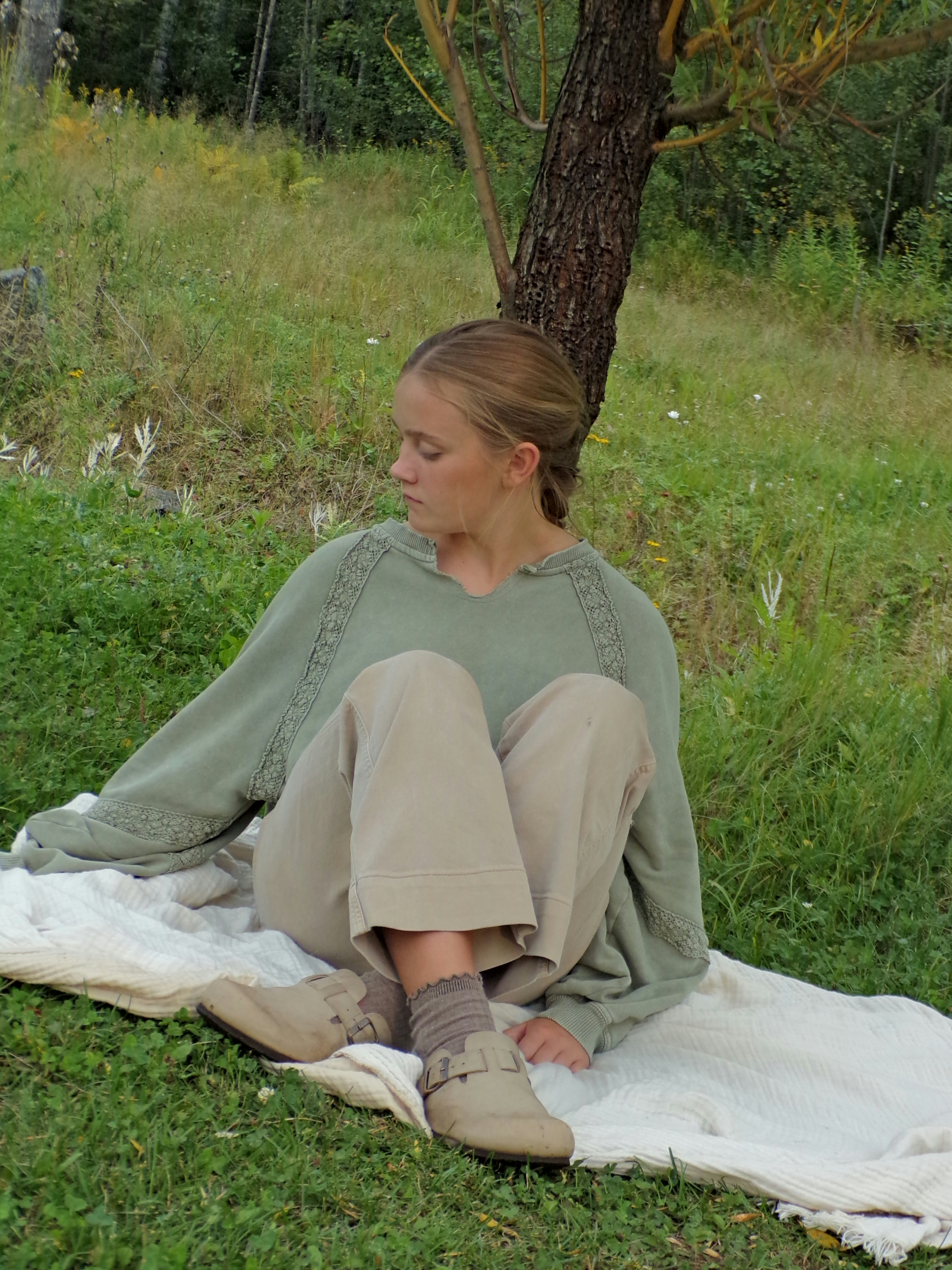 Young woman sitting on blanket under tree