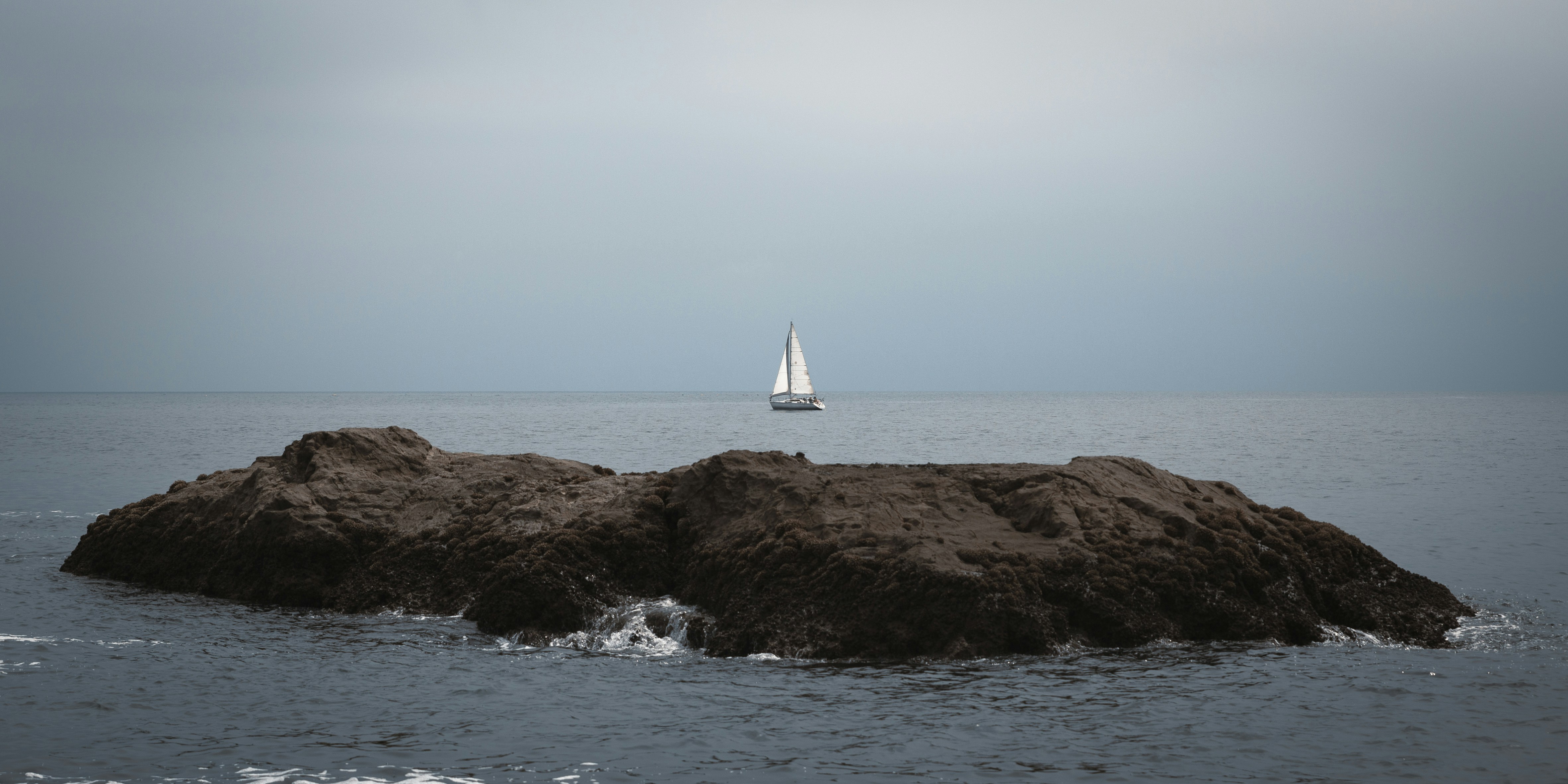 A sailboat sails on the ocean near a rocky island.