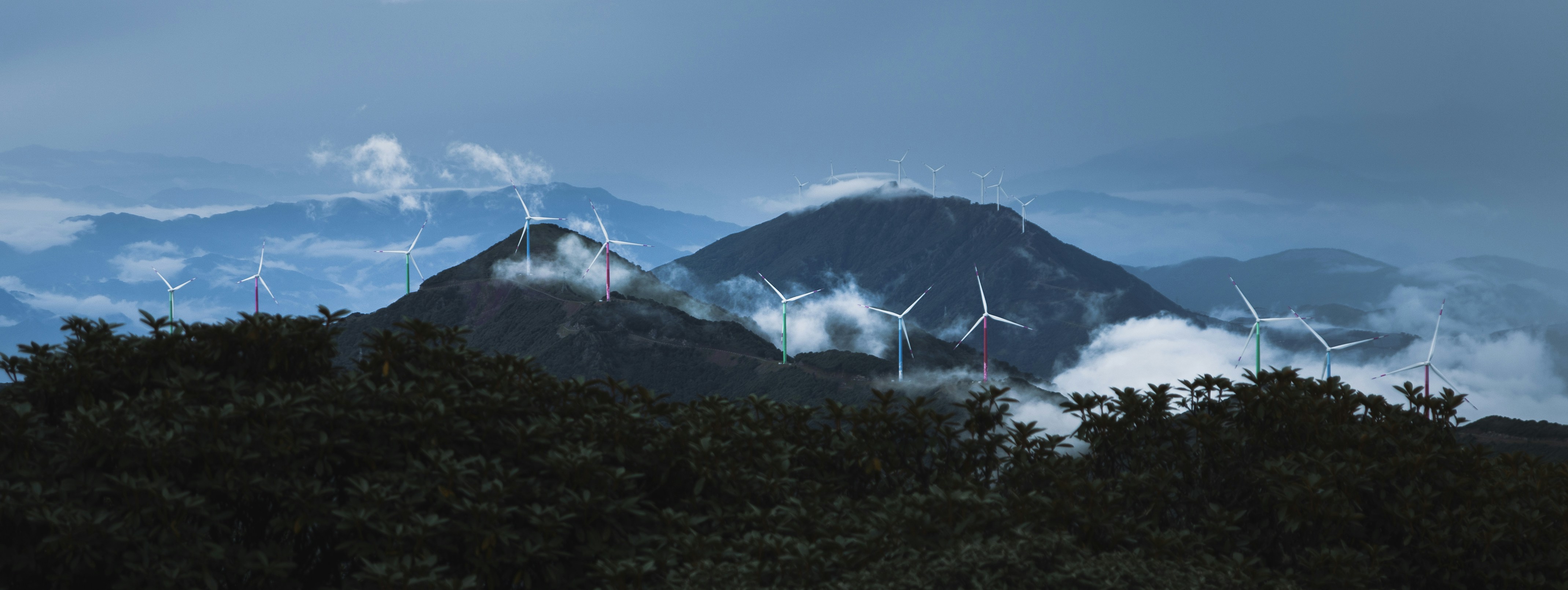 Wind turbines on misty mountains under a blue sky.