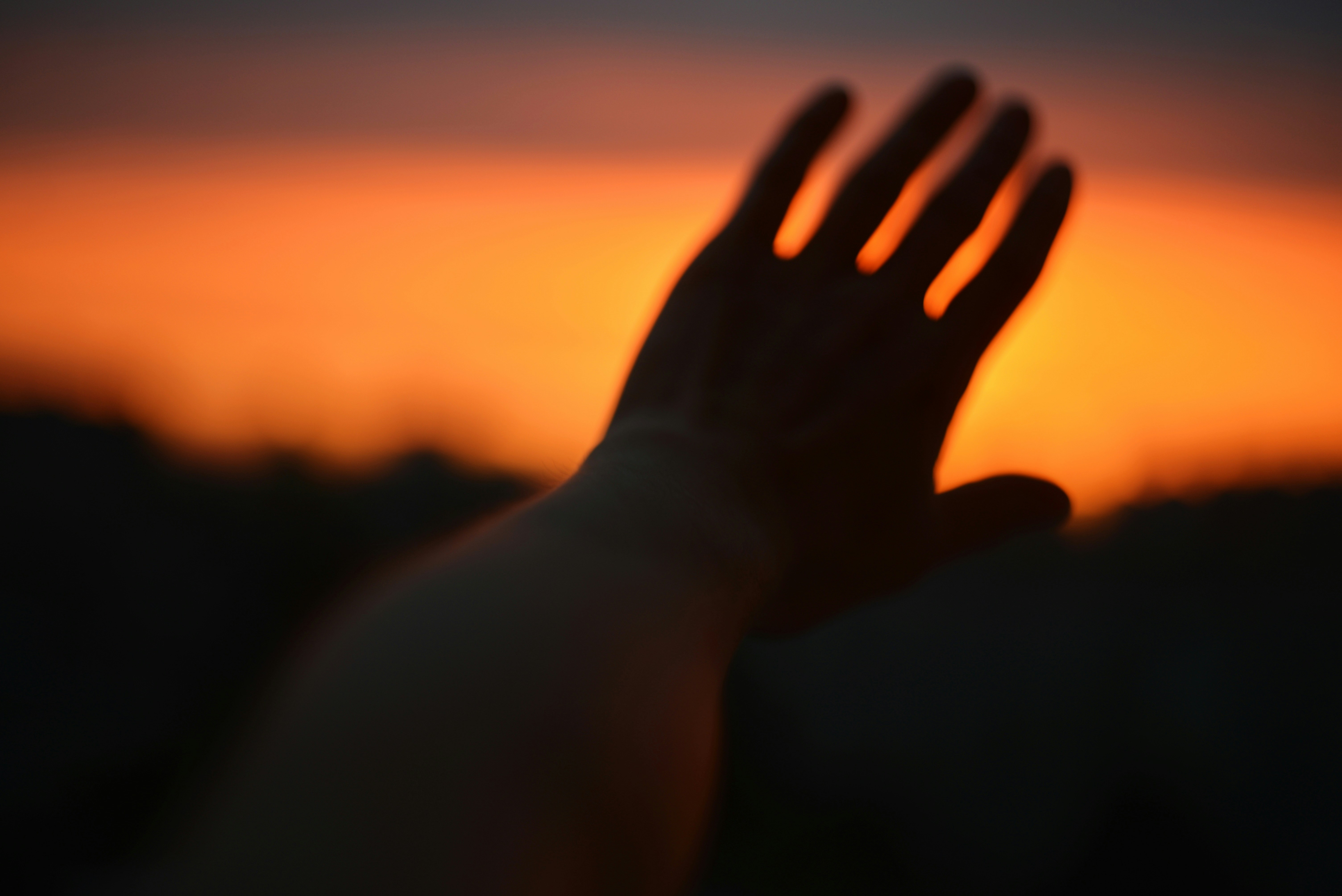 Hand reaching towards a vibrant sunset sky.