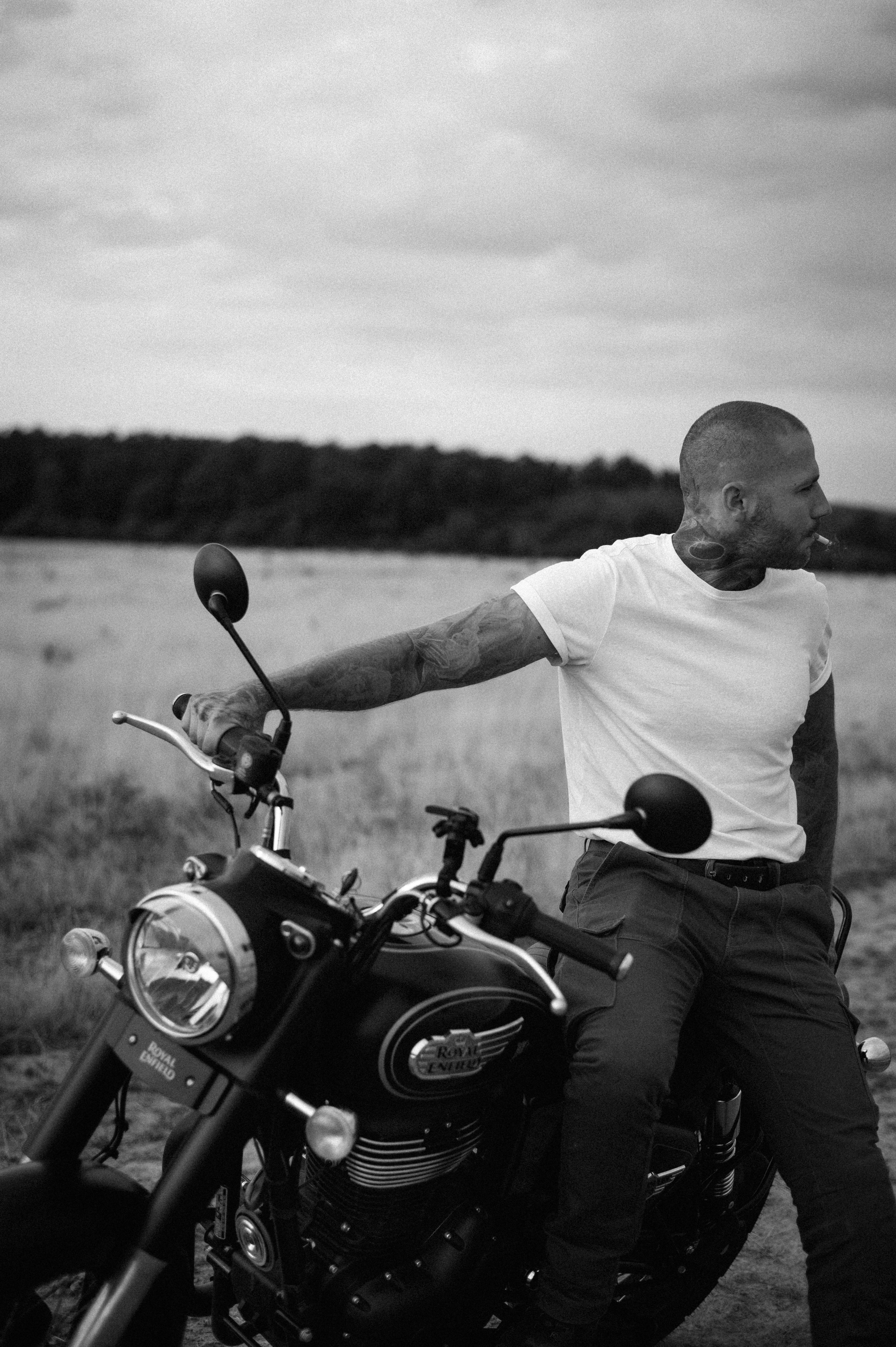 Edge of the Field: A Tattooed Rider Pauses by a Classic Motorcycle