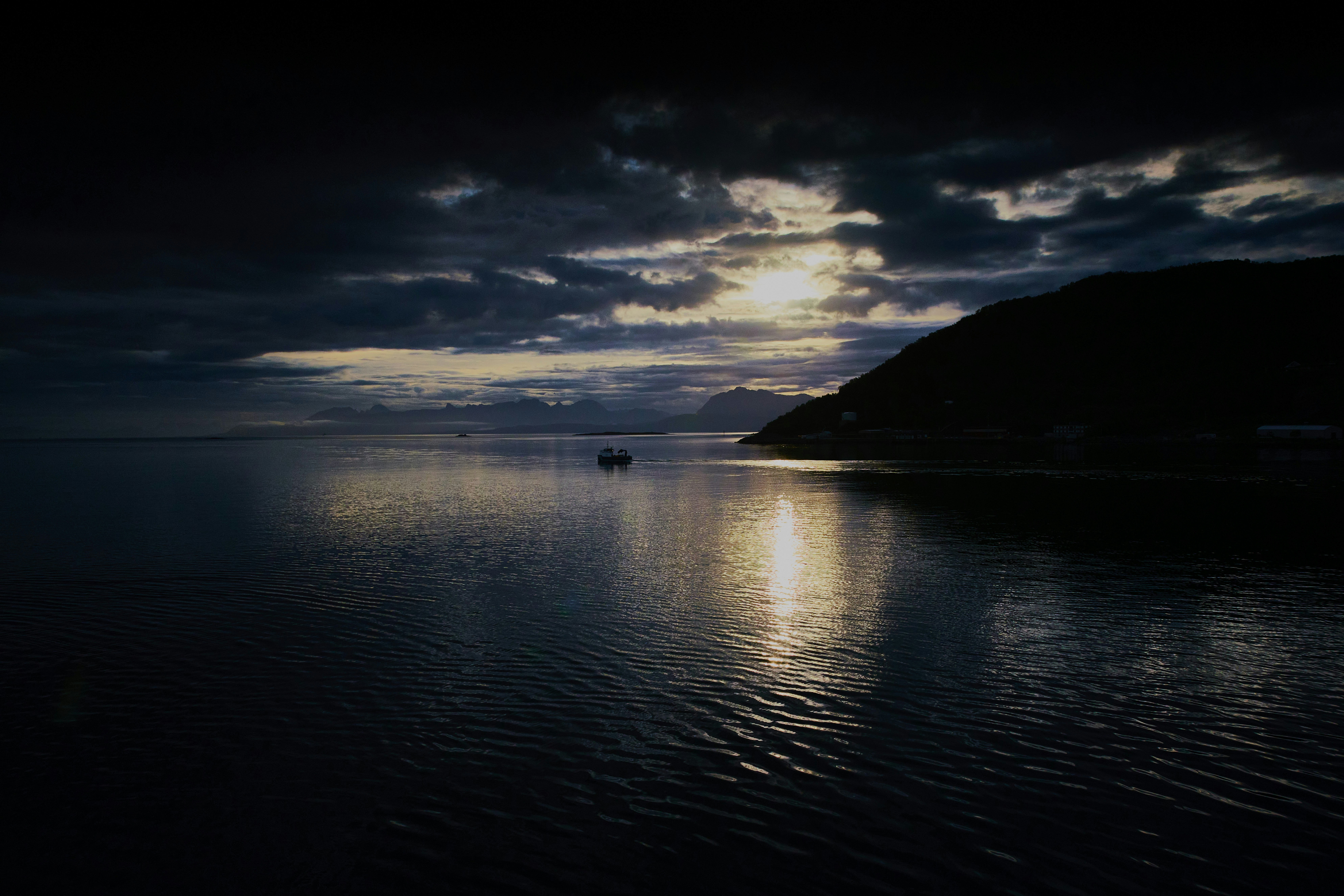 A serene seascape at dusk, featuring a small boat gliding across the reflective surface of the water under a dramatic sky.