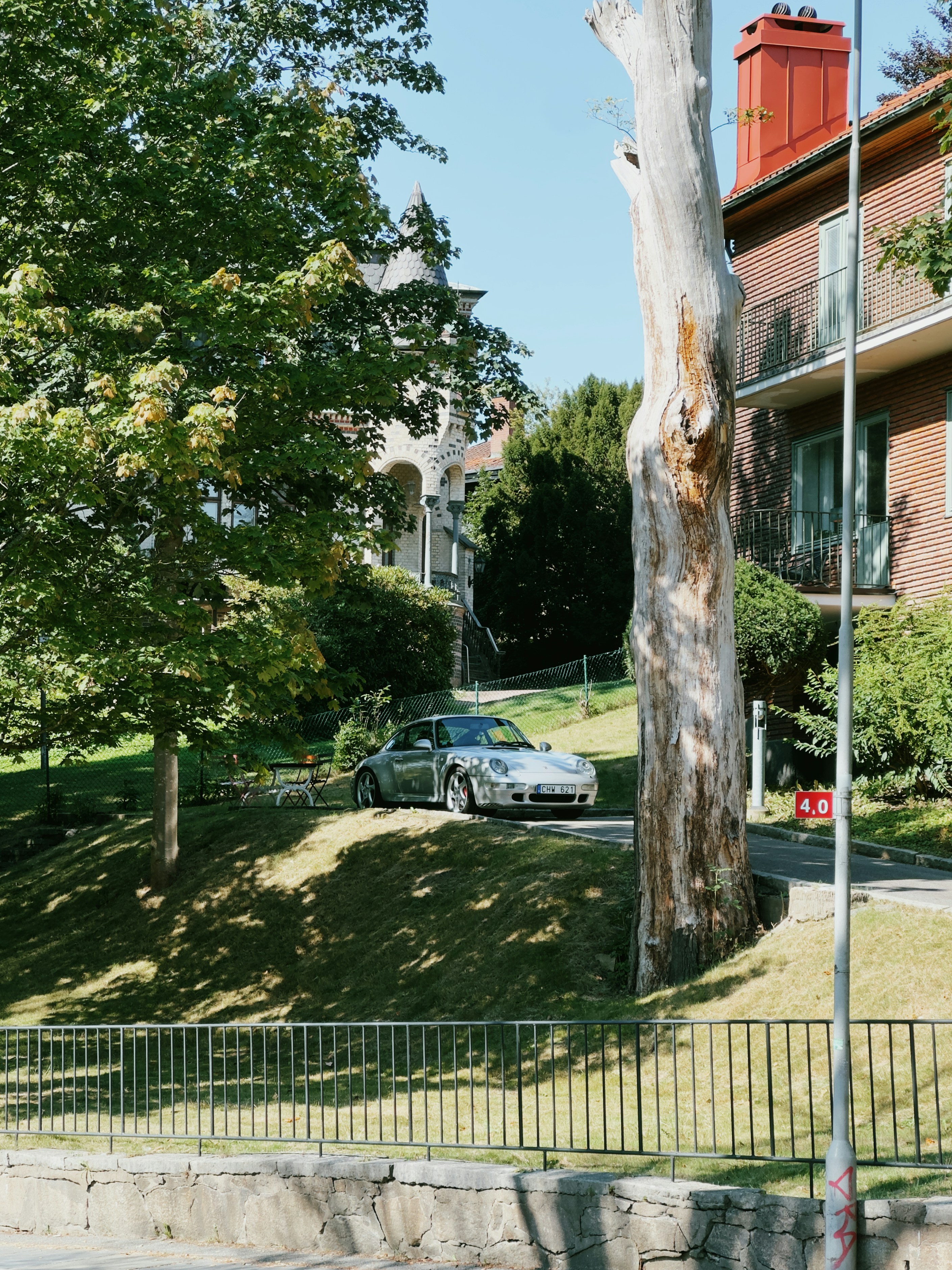 Silver sports car parked on grassy hill near trees.