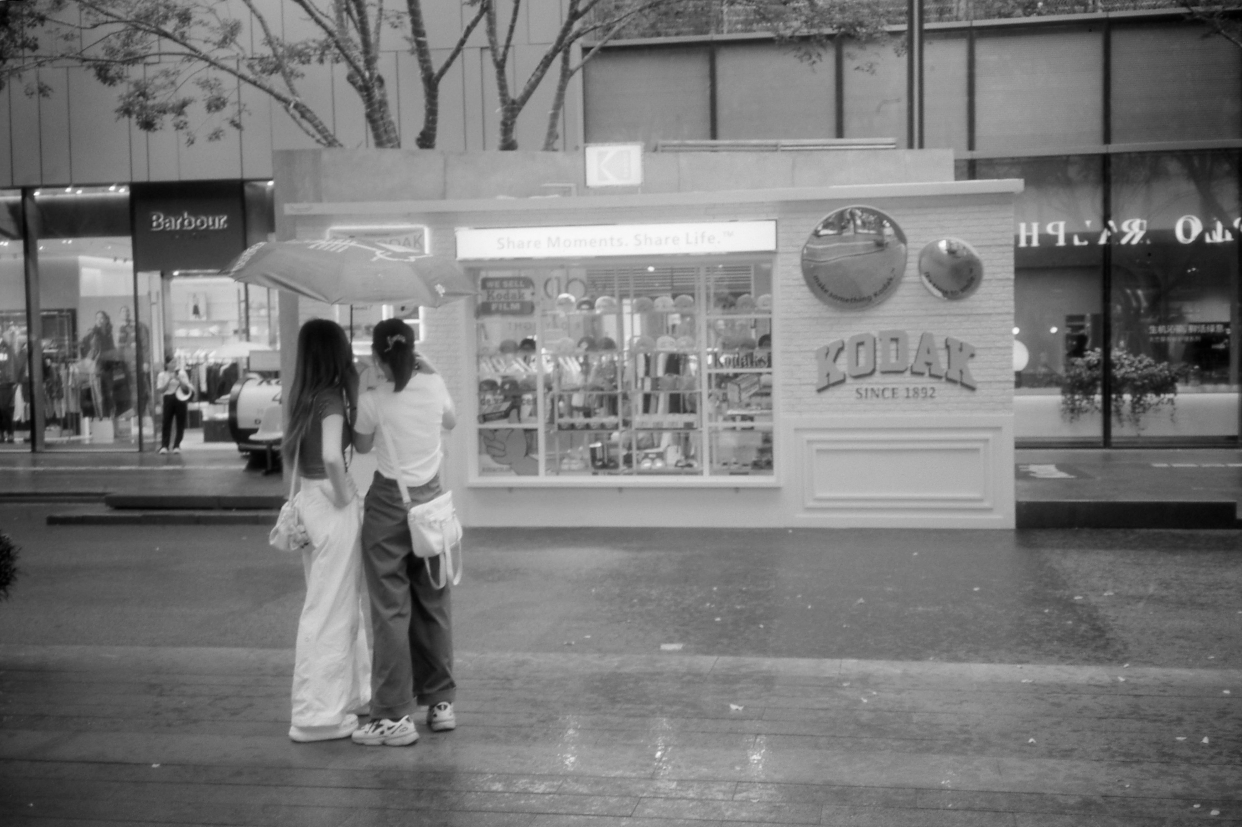 Kodak set up a pop-up store offline, but unfortunately, it started raining when I went there. | Two people share an umbrella in the rain.