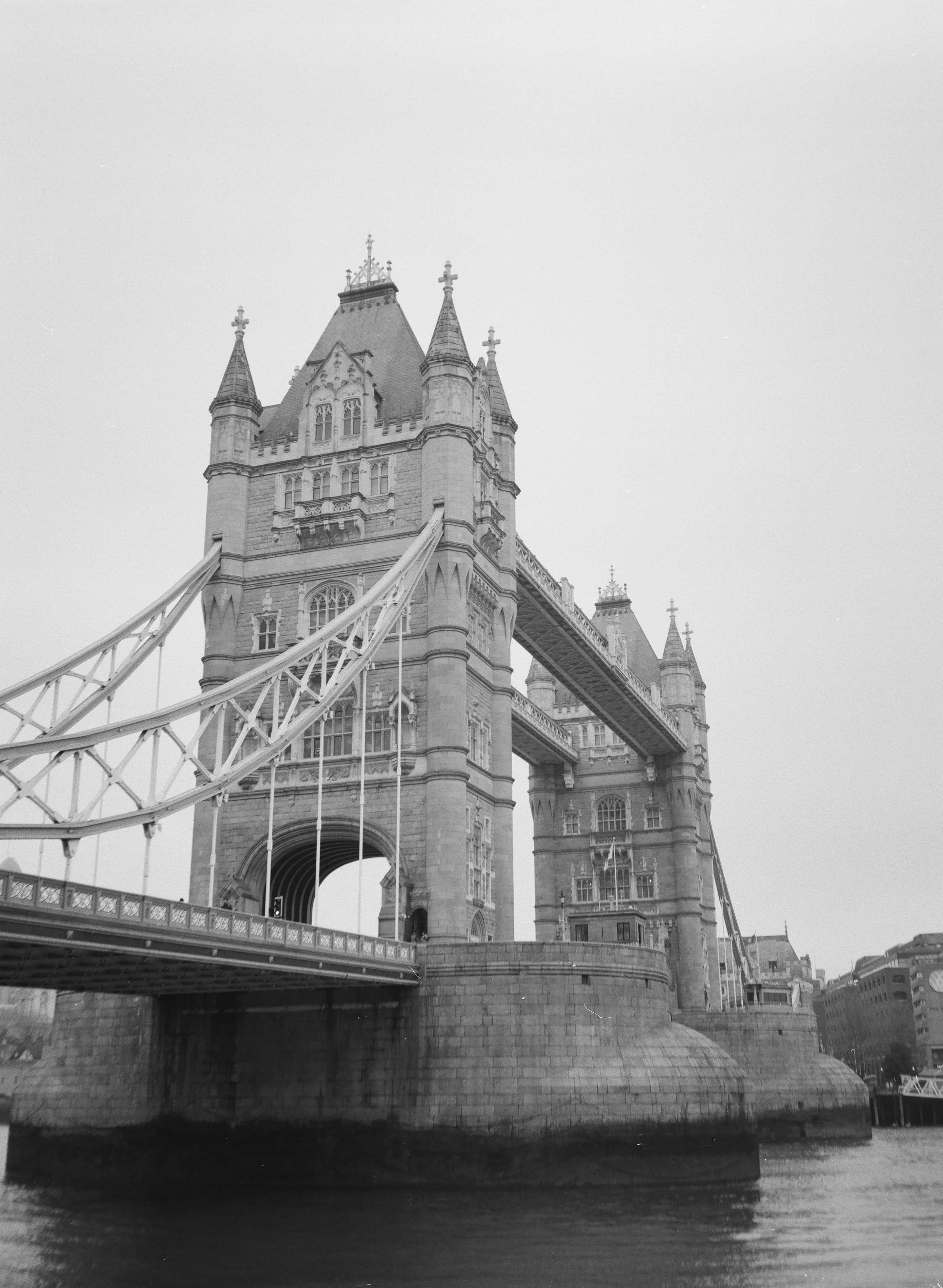 Tower Bridge stands majestically over the River Thames, showcasing its intricate architectural details in monochrome. The iconic suspension cables and towers evoke a sense of historical grandeur.