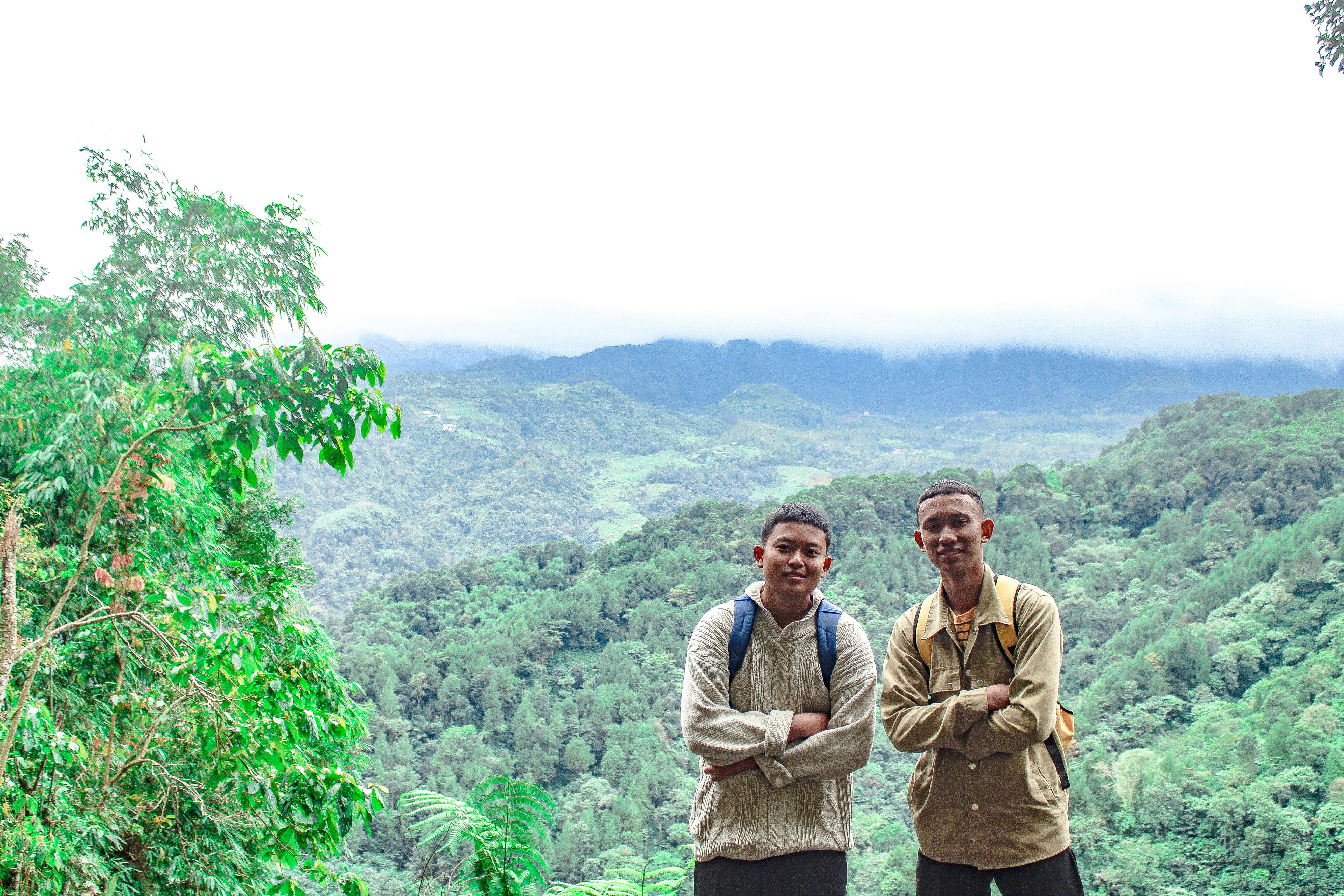 Two young men stand with arms crossed on a hill.