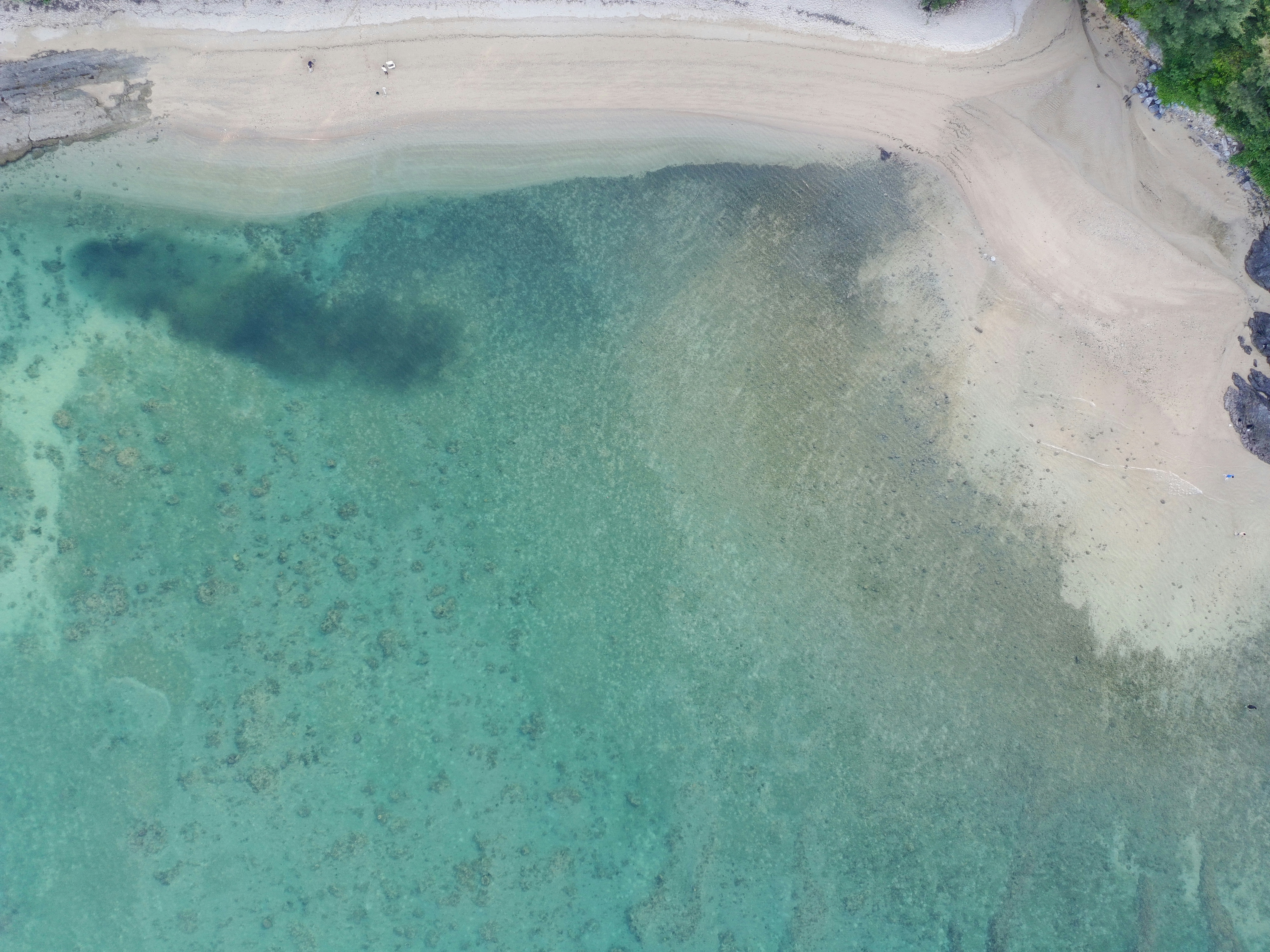 Aerial view of a tranquil beach with clear turquoise waters and a sandy shoreline, showcasing the natural beauty of the coastline.
