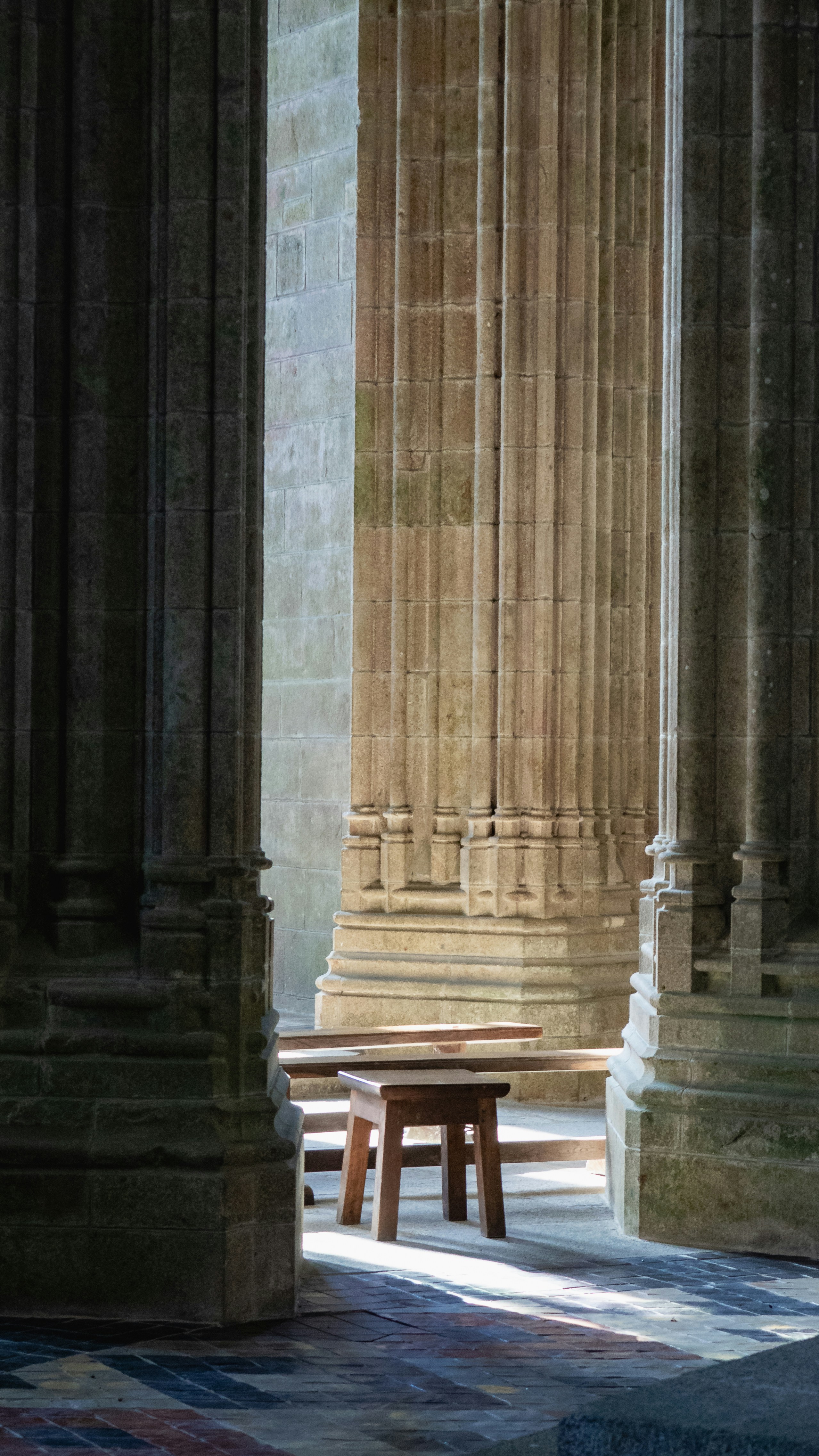 Sunlight streams through a cathedral's columns, illuminating a solitary wooden table amidst the ancient stone architecture.