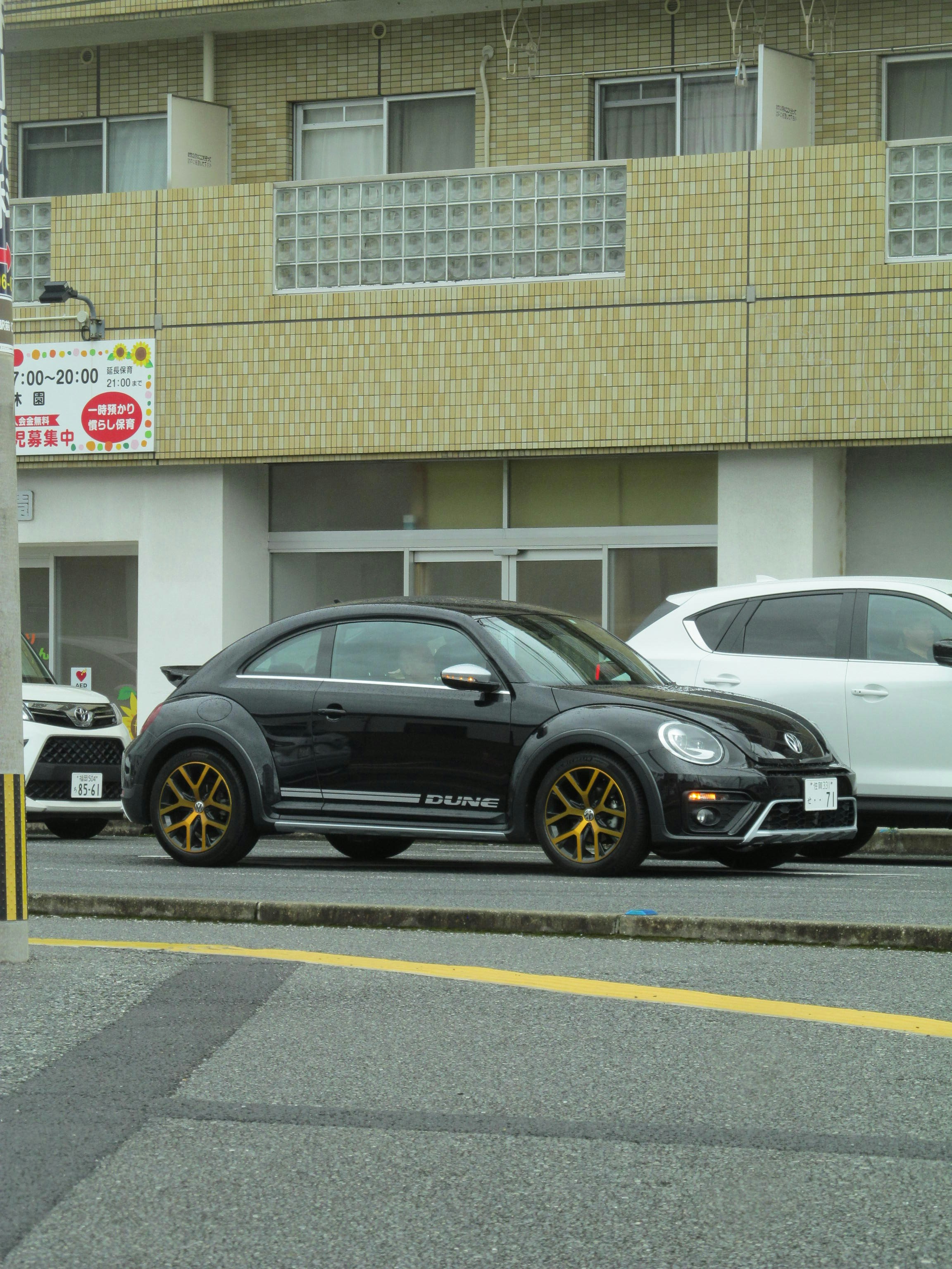 A customized black Volkswagen Beetle Dune parked alongside other vehicles in a city setting, showcasing its unique design and sporty wheels.