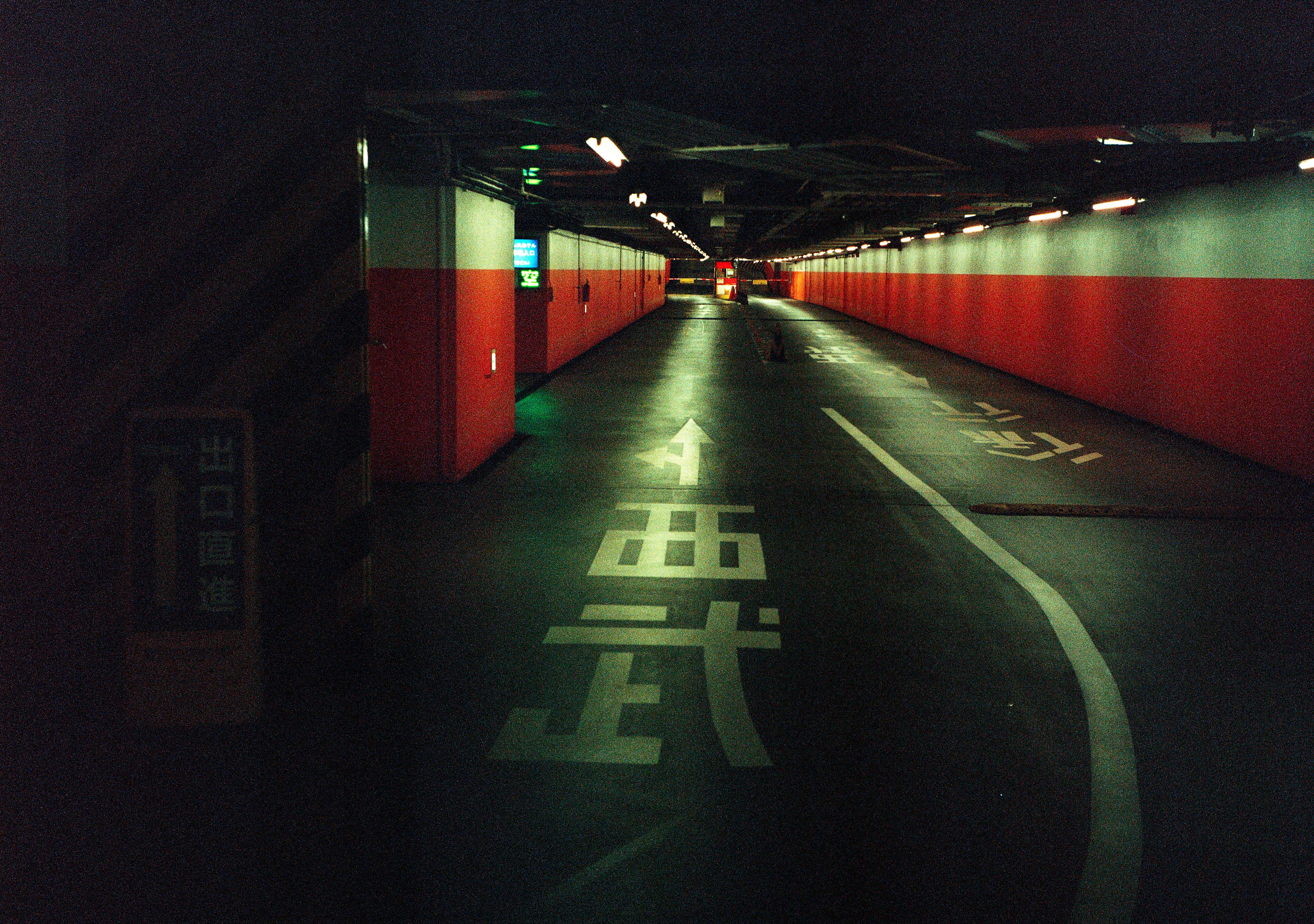 A dimly lit underground parking garage featuring vibrant red walls and illuminated directional markings on the ground.