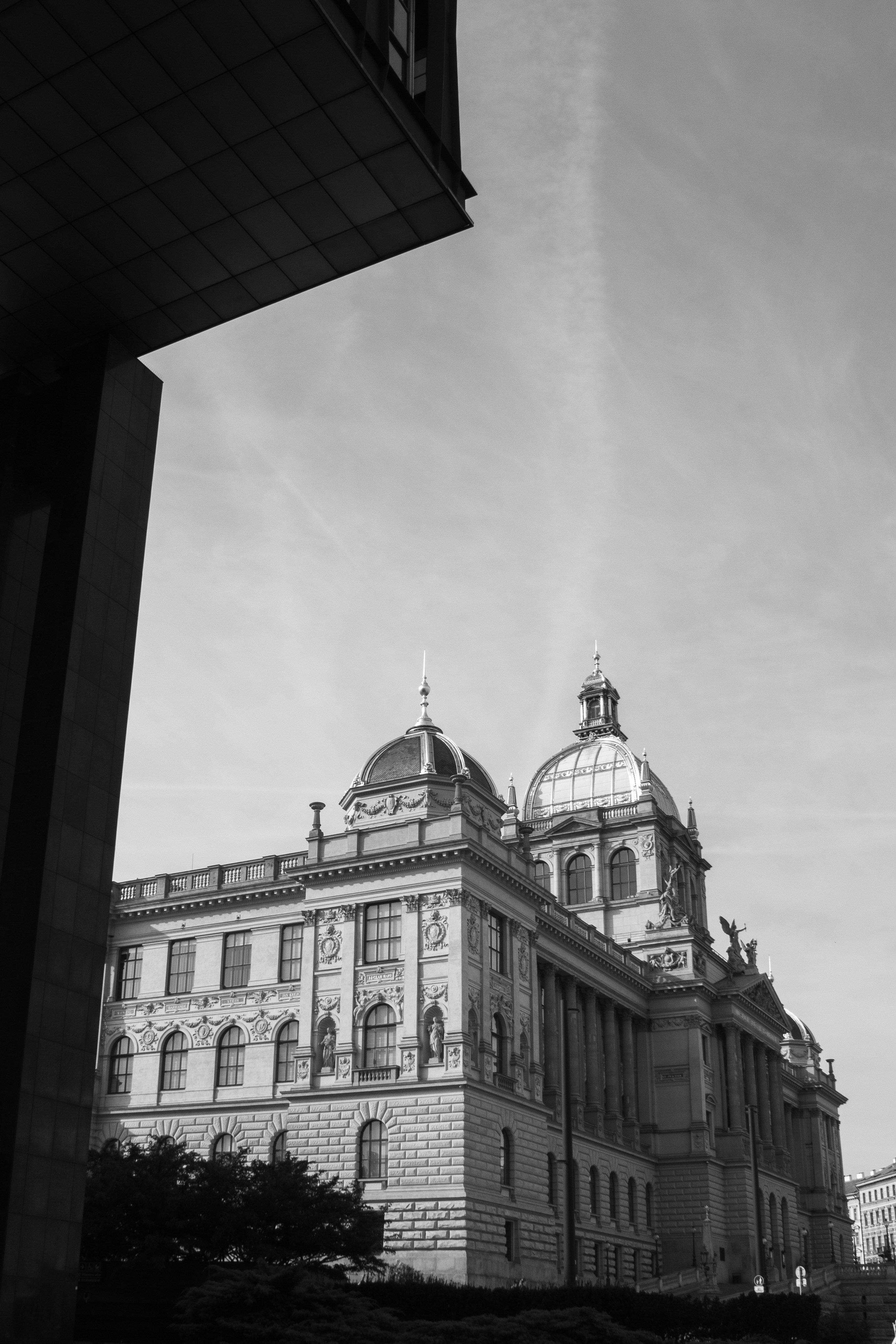 Historic building featuring ornate domes and intricate detailing, framed by modern architecture. Black and white tones enhance the structure's timeless appeal.