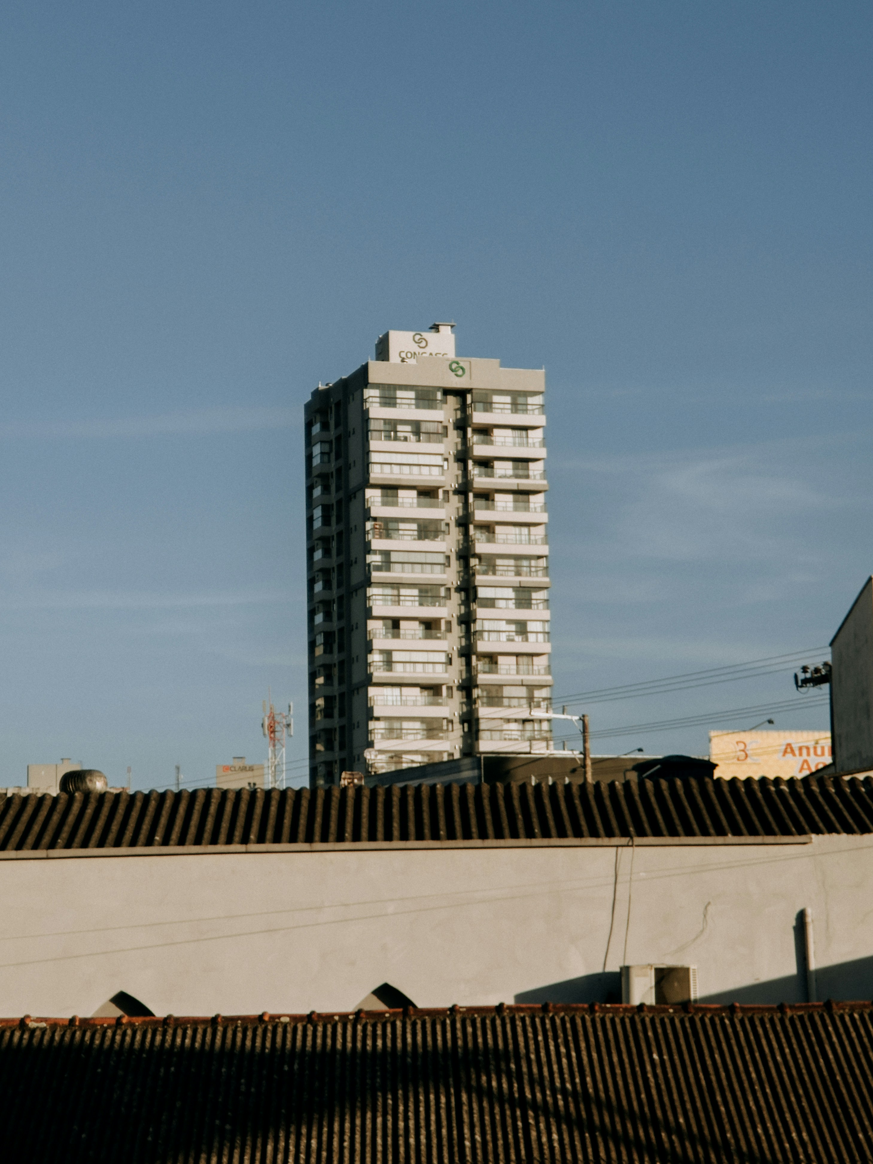 A contemporary apartment building rises above older rooftops, showcasing a blend of architectural styles in an urban landscape.
