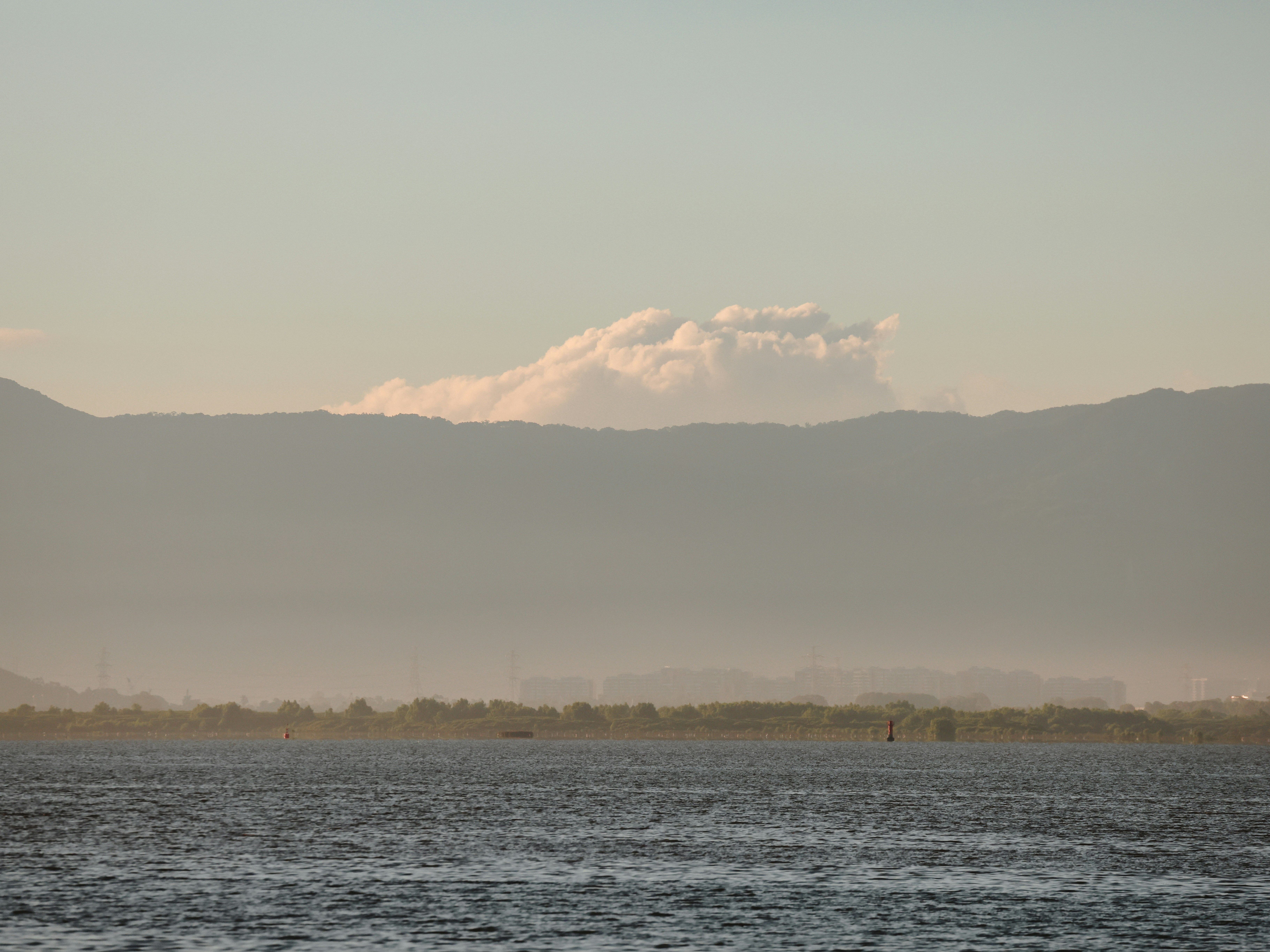Softly layered mountains fade into the distance, kissed by clouds, while a tranquil waterway reflects the gentle light of dusk.